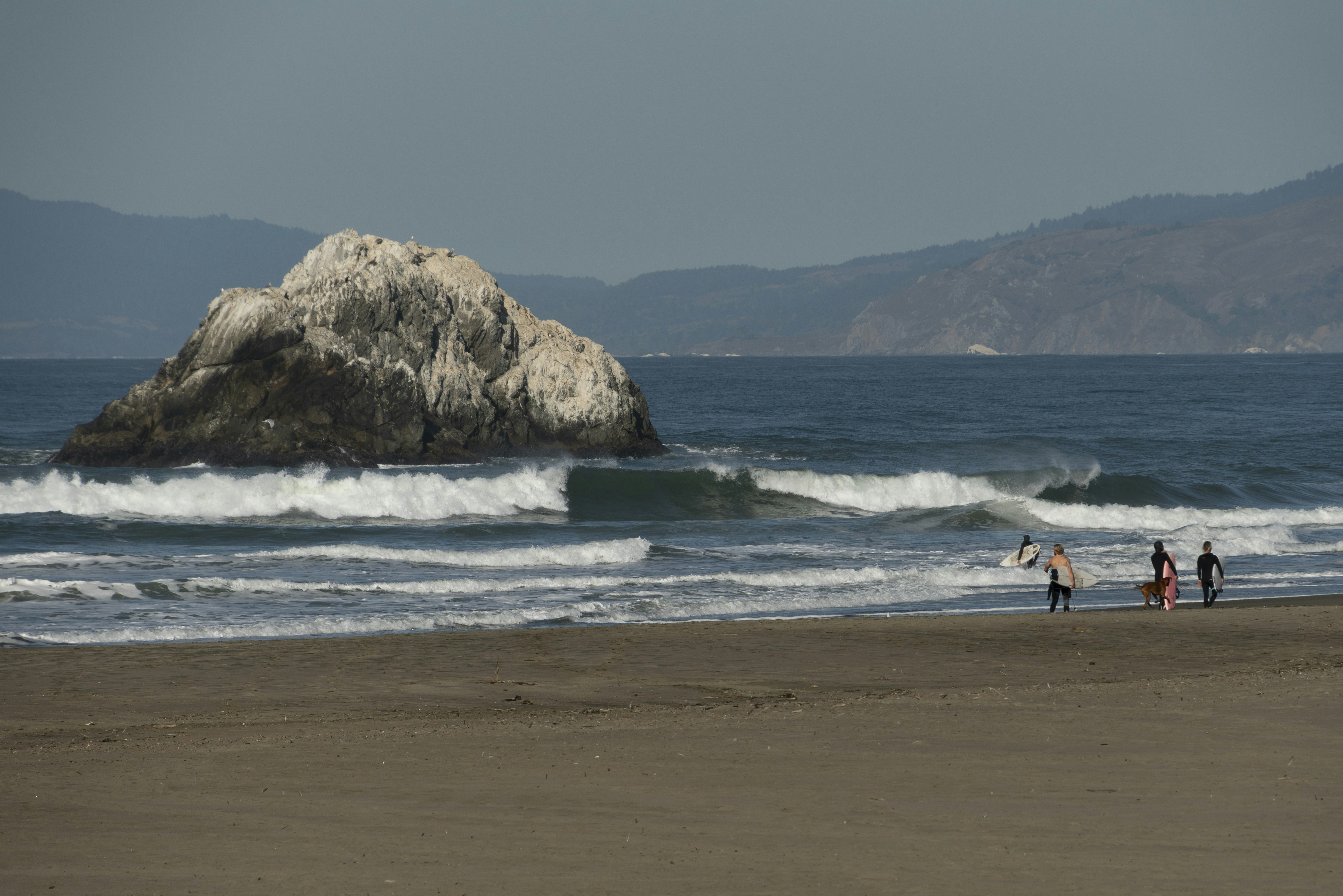 Rock Outcrop Stands Watch Over a Quiet Shore as Surfers Gather