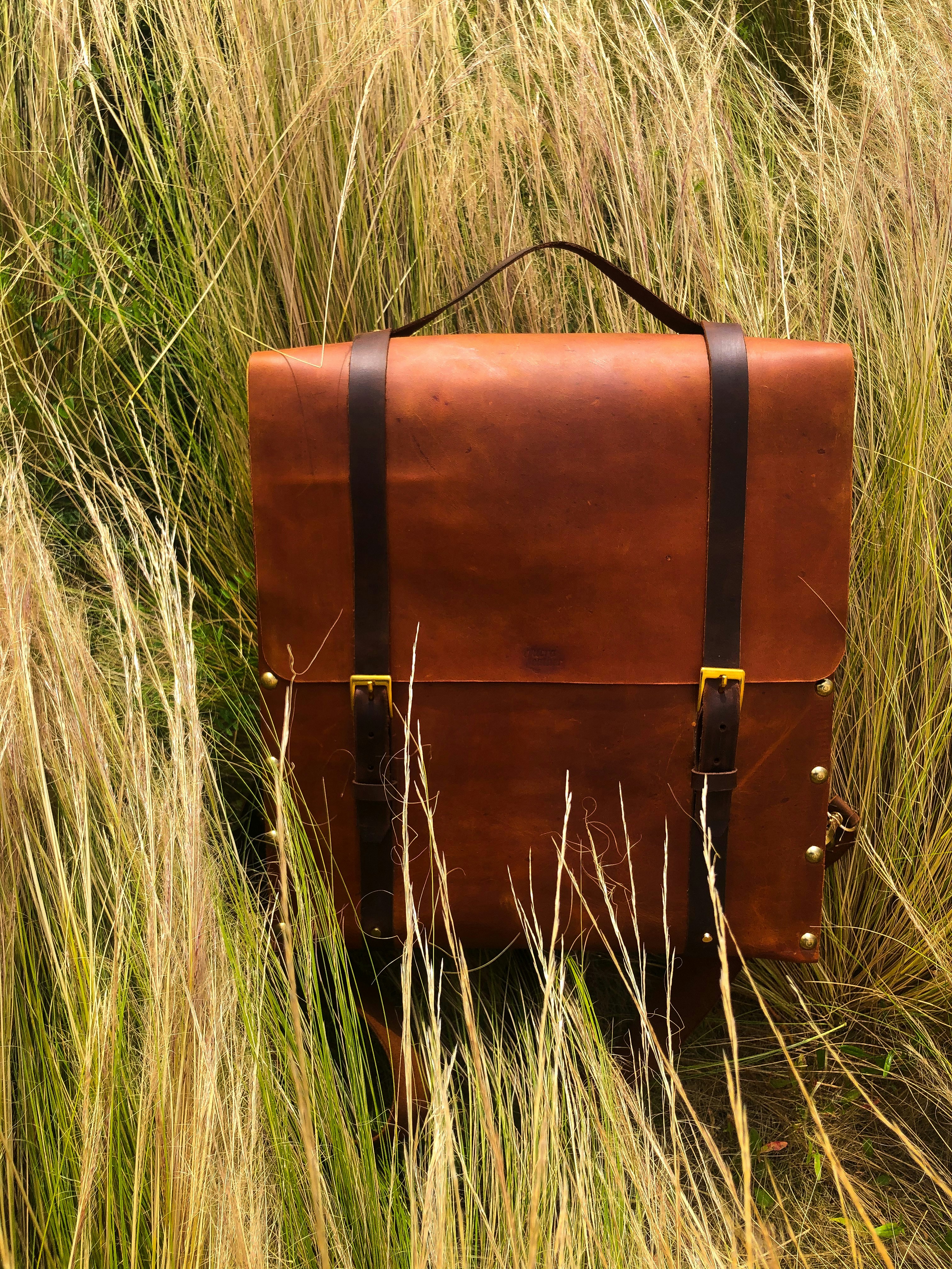 A handcrafted leather satchel rests among tall, golden grasses, showcasing its rich texture and craftsmanship.