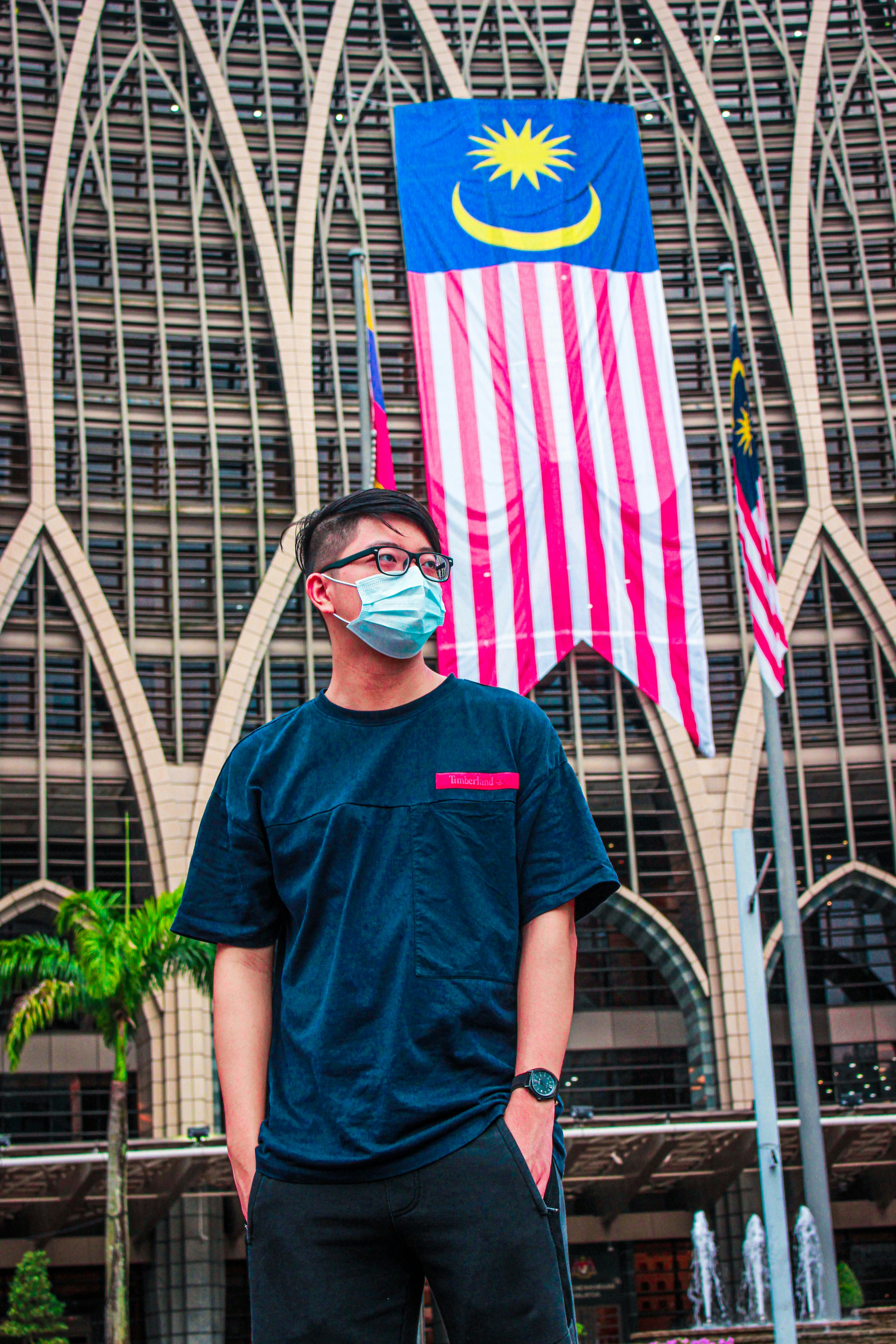 man in blue crew neck t-shirt standing near flag of us a during daytimeK X I T H V I S U A L S