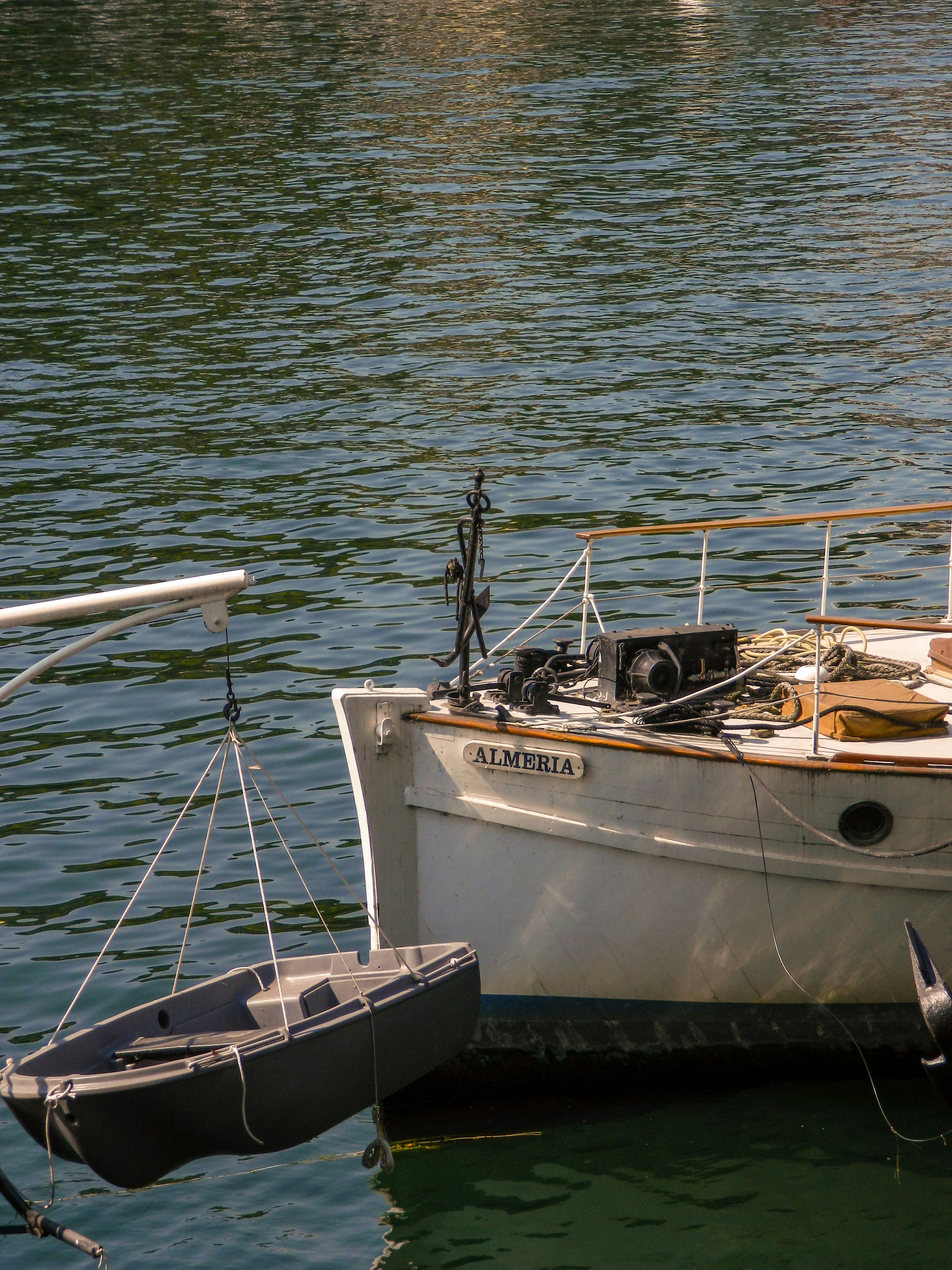 A white fishing boat named 'ALMERIA' anchored by the shore, accompanied by a small dinghy, reflecting the calm waters of the harbor.
