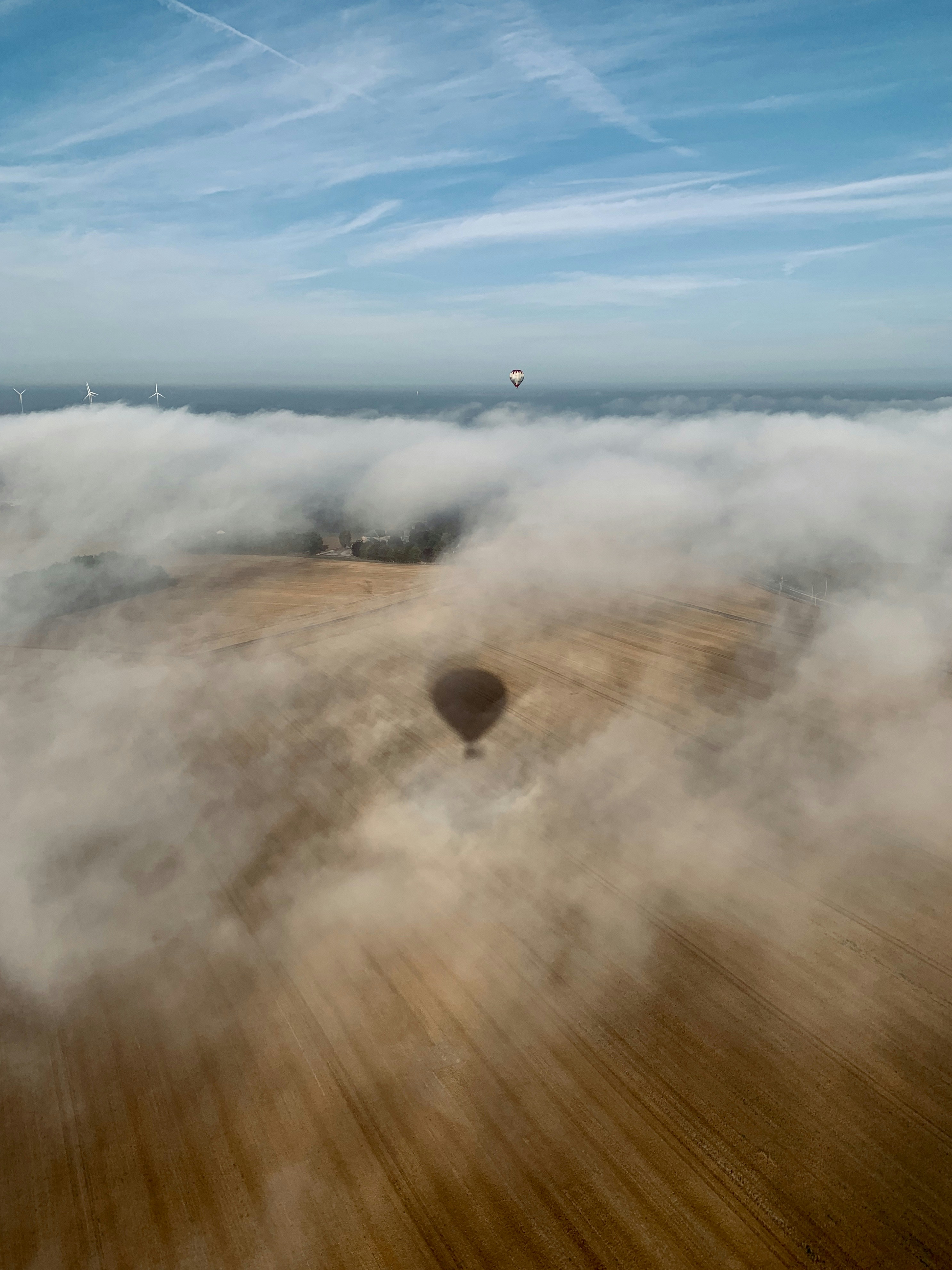 Aerial Dawn: A Balloon Drifts Above Cloud Veils Over Painted Fields