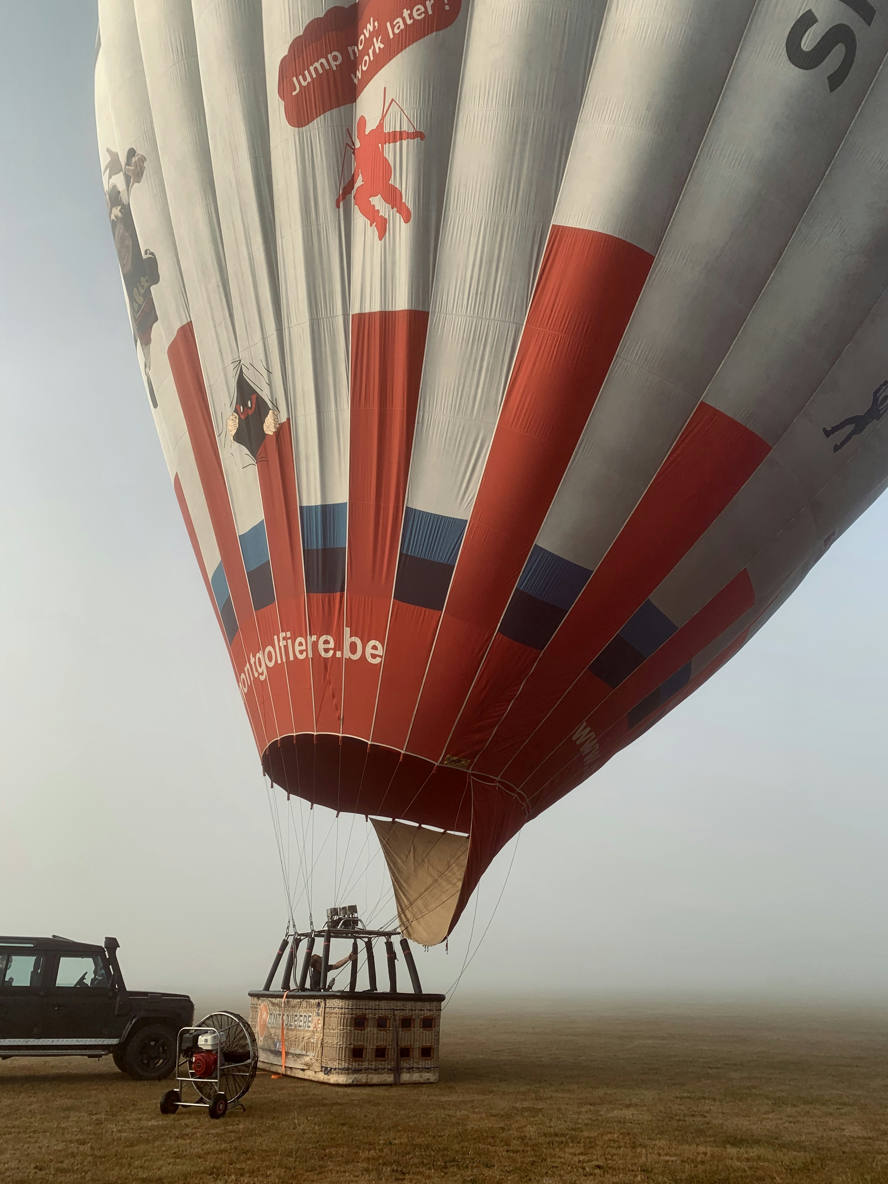 A vibrant hot air balloon prepares for takeoff amidst a foggy landscape, showcasing its colorful design and the equipment used for inflation.