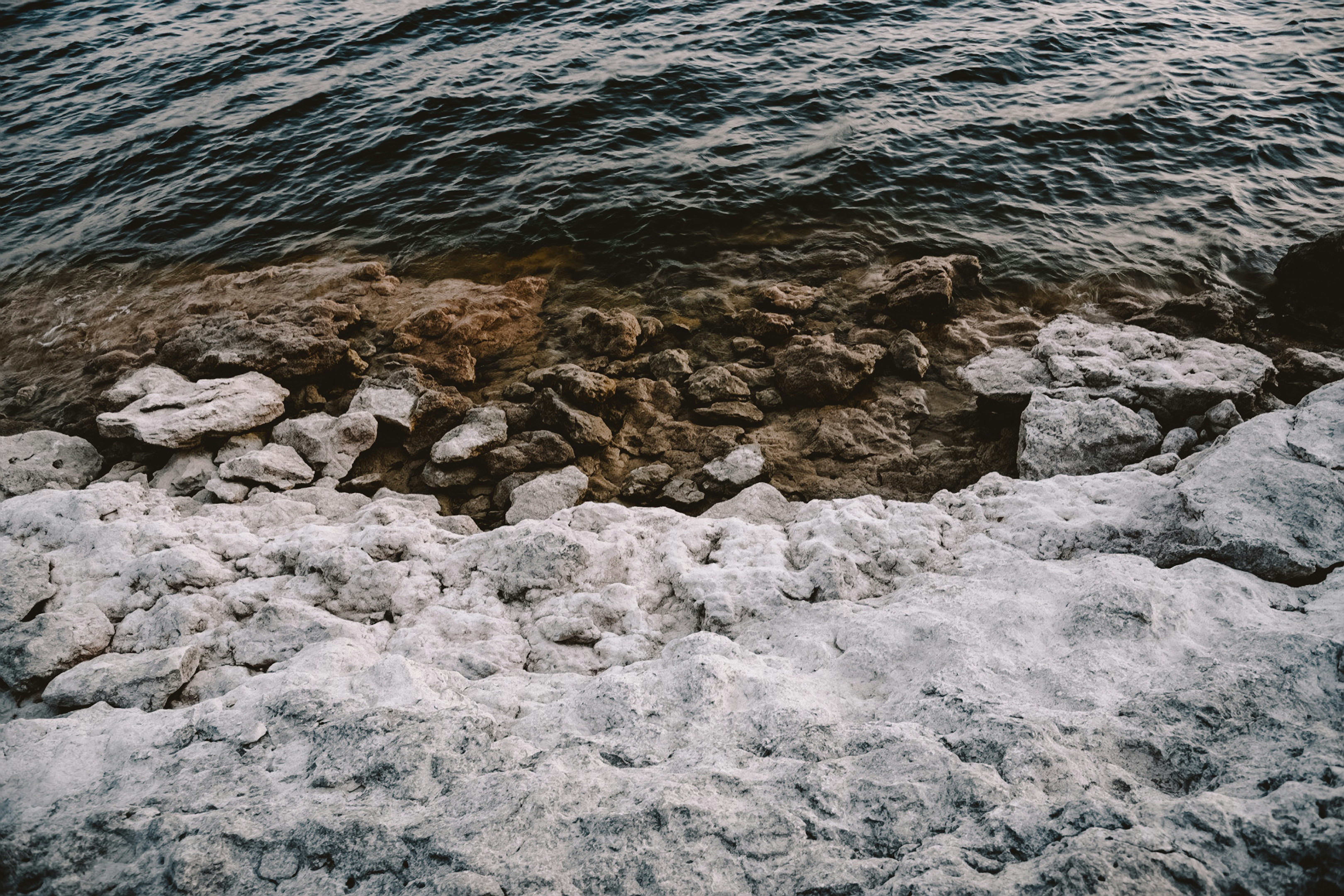 Rocky shoreline meeting calm waters, showcasing a blend of textures and natural elements. The contrast between the stones and water creates a serene atmosphere.