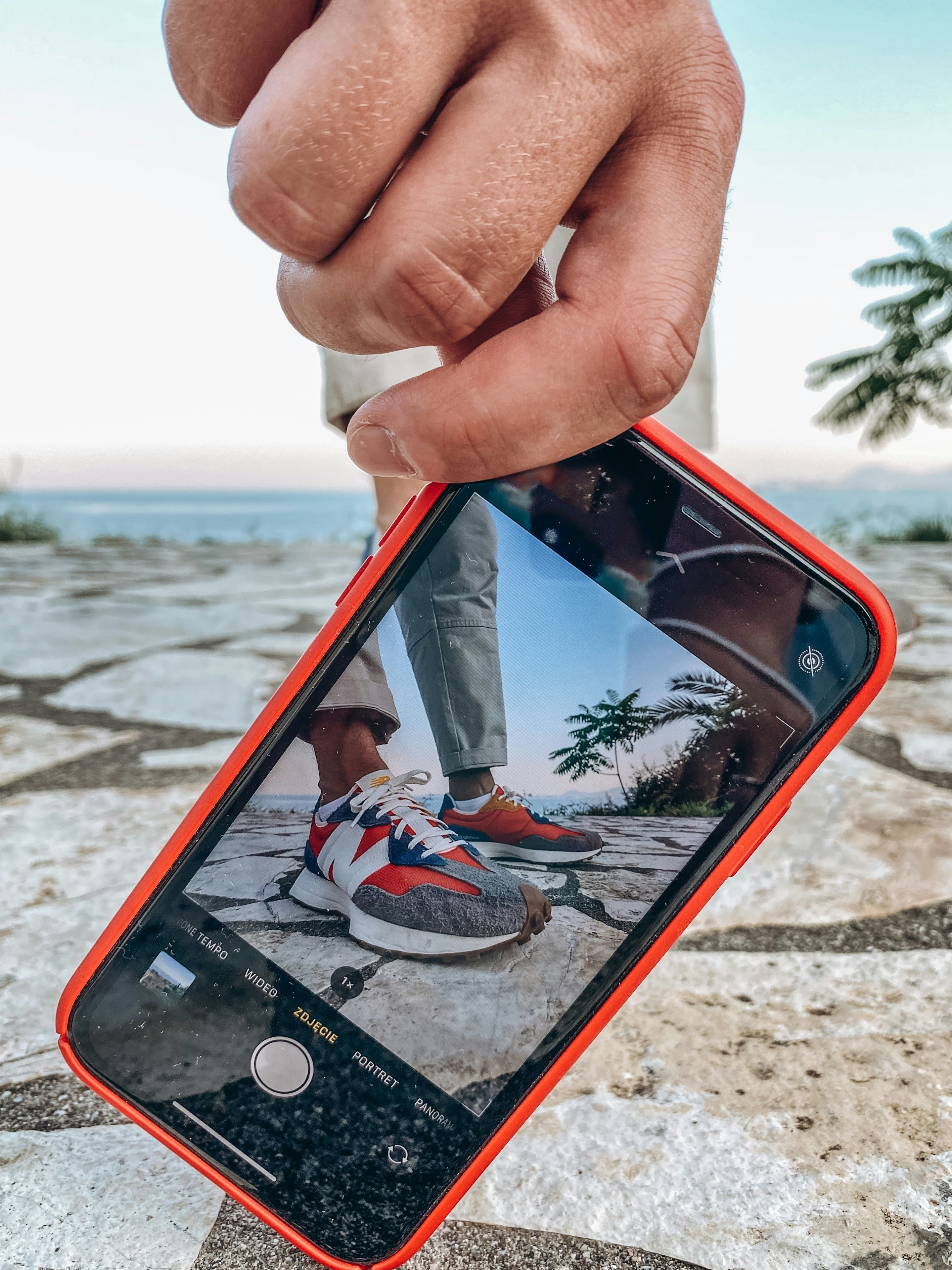 Red-Soled Moment: Hands and Phone in Focus on a Sunny Boardwalk