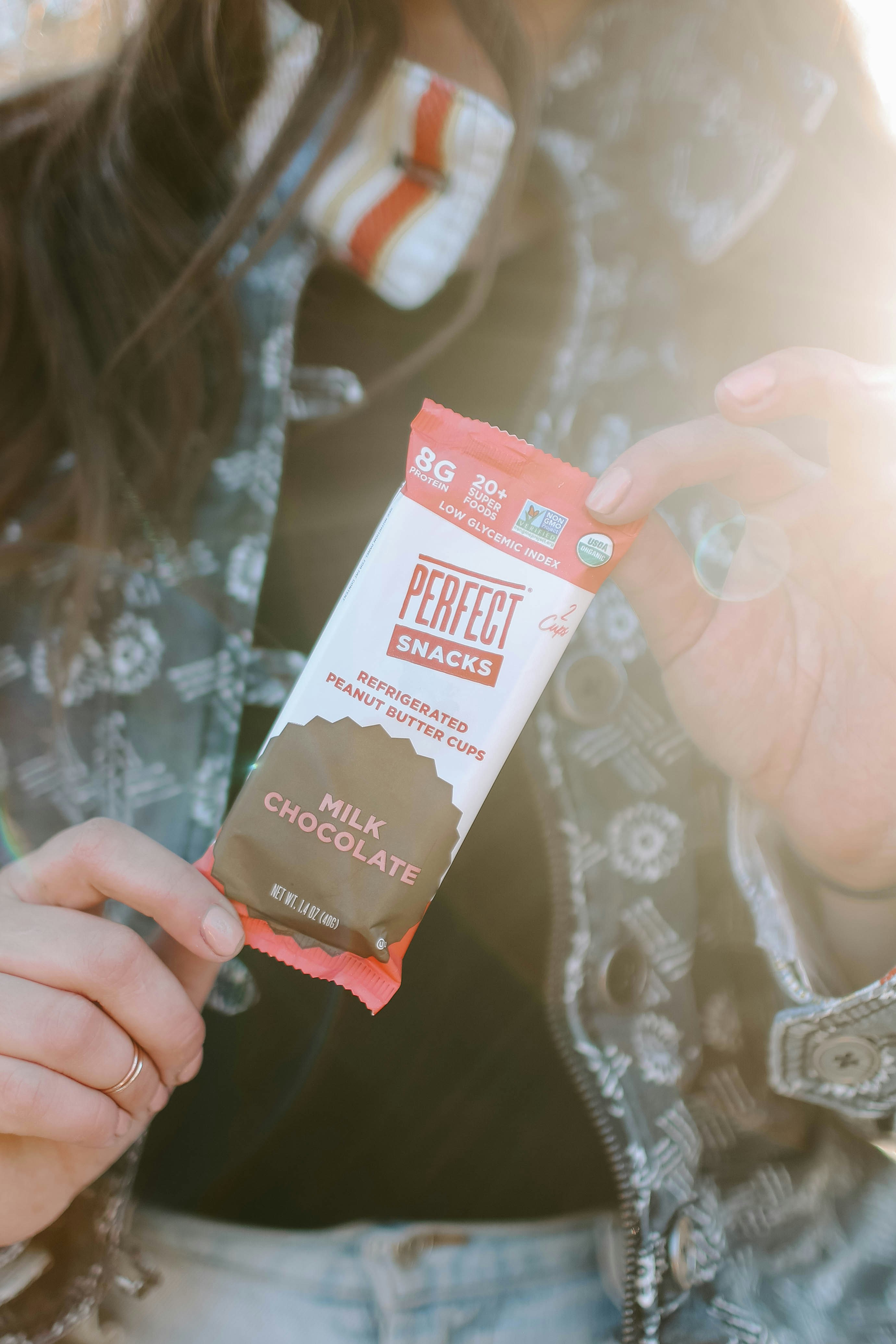 Hand holding a Perfect Snacks refrigerated peanut butter cup in milk chocolate against a softly lit background.