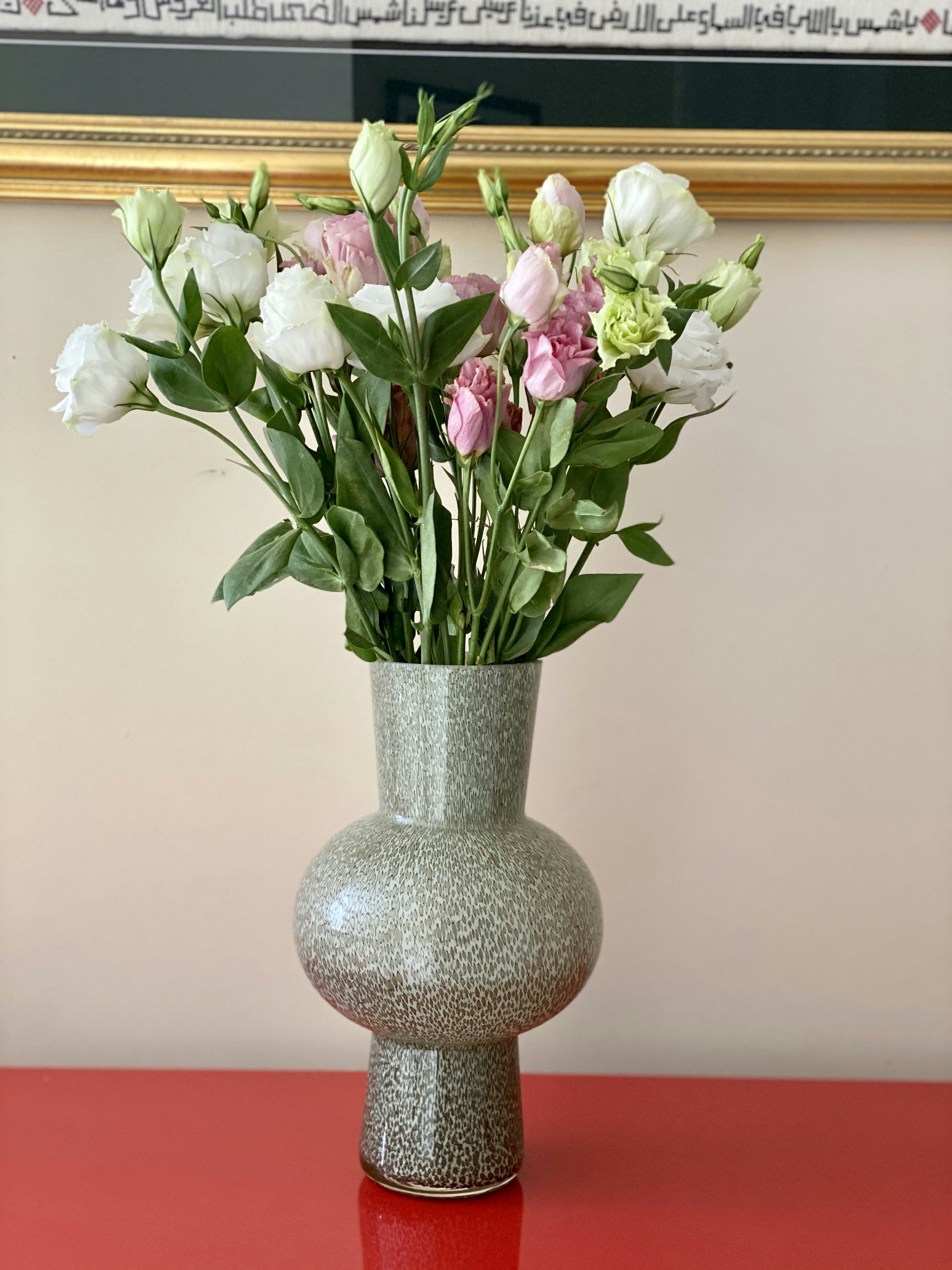 A bouquet of pastel flowers arranged in a textured vase, set against a soft background. The composition highlights the delicate colors and forms of the blooms.