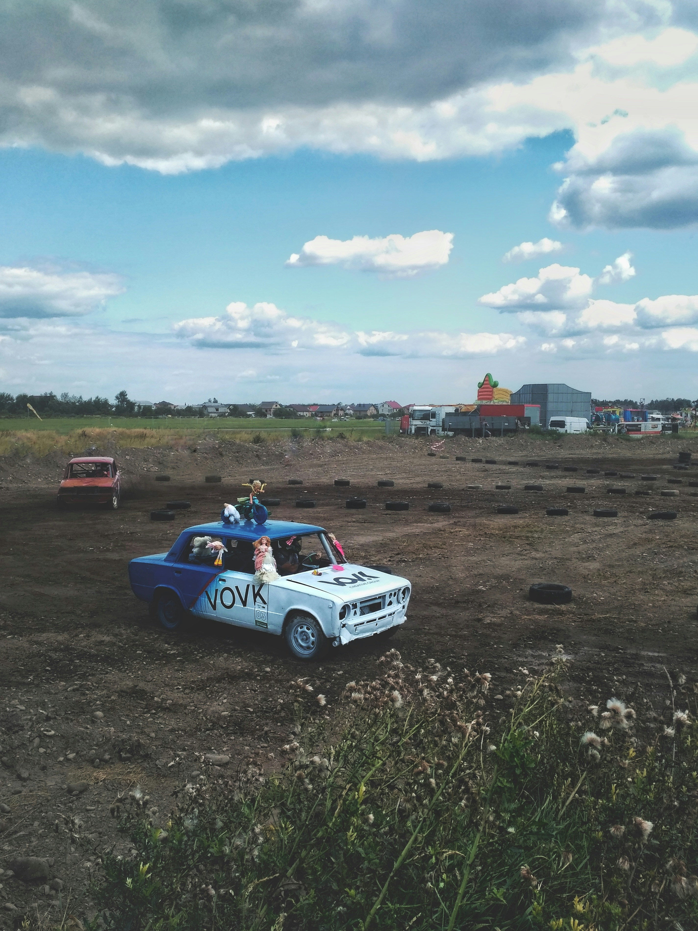 blue and red porsche 911 on brown field under blue and white cloudy sky during daytime