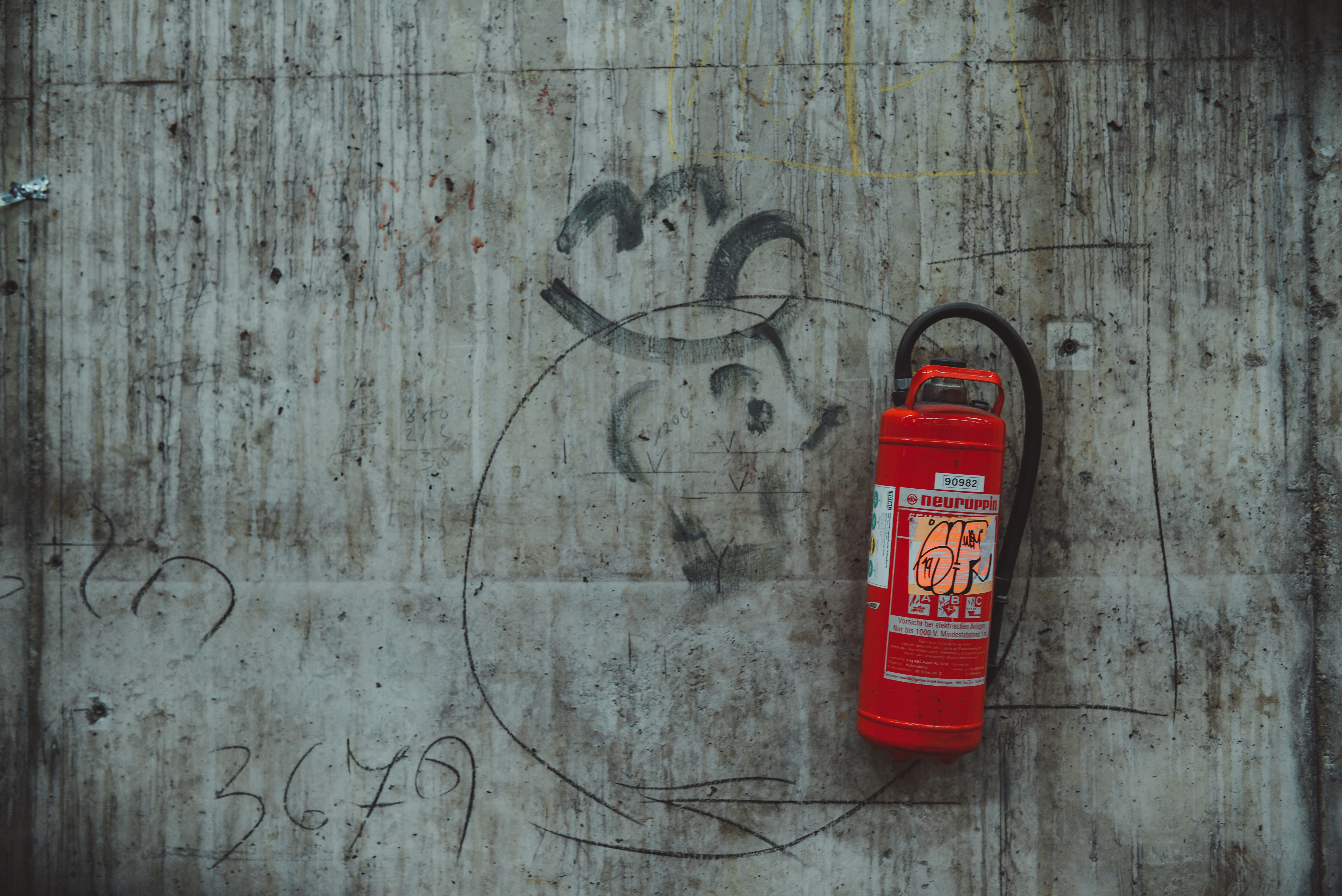 Scarlet Anchor on a Weathered Wall: Fire Extinguisher Amid Graffiti