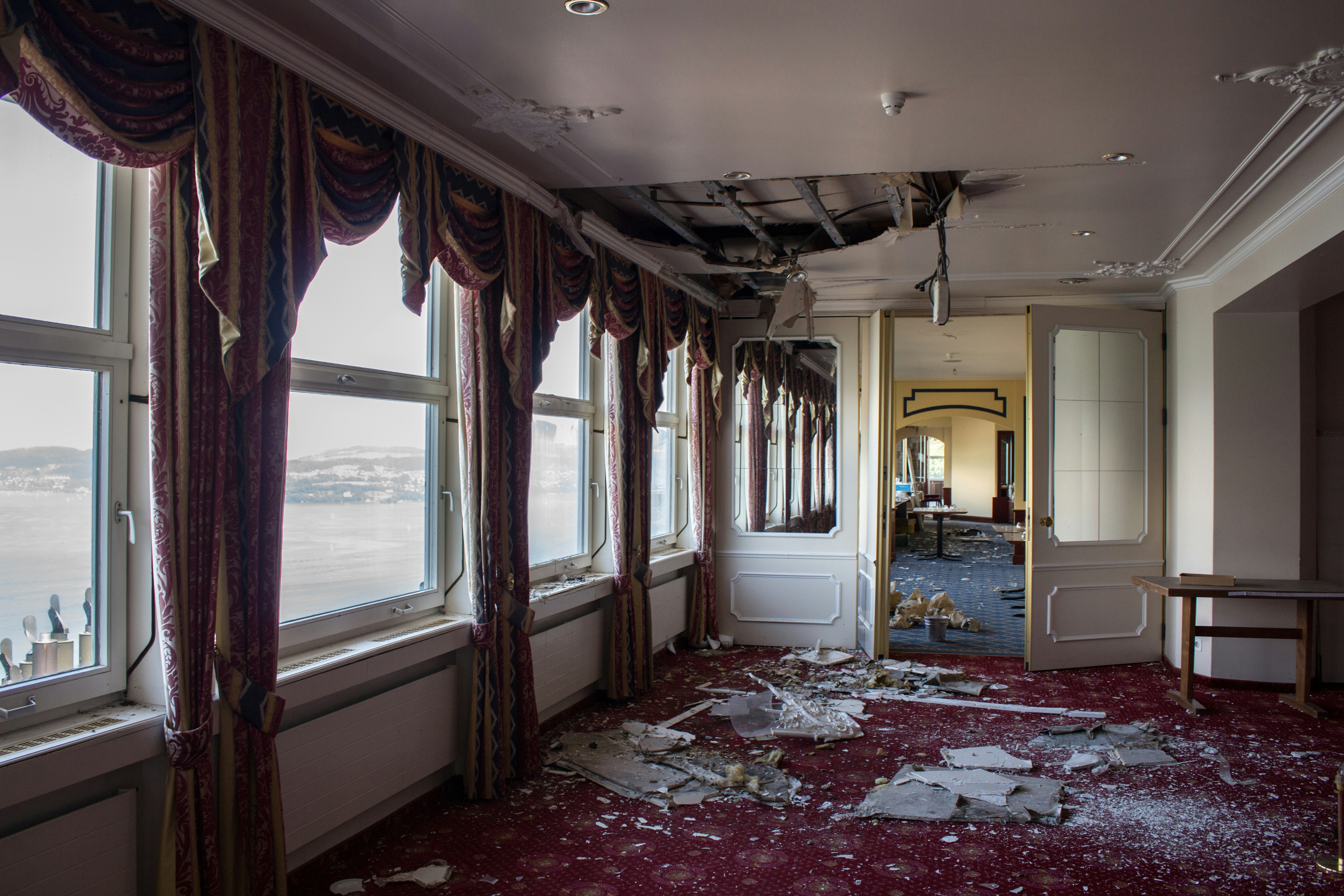 Empty Ballroom After the Storm: Sunlit Windows, Frayed Curtains, and a Silent Corridor