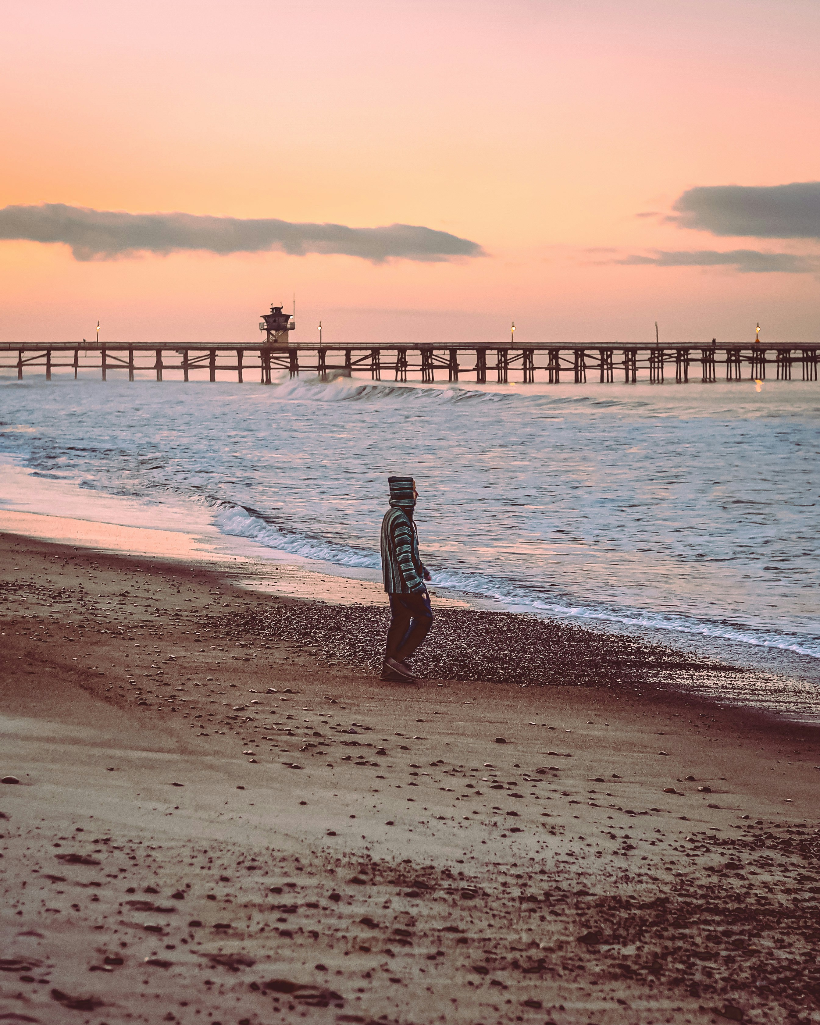 Footsteps at Quiet Tide: A Lone Visitor Beneath a Sunset Pier