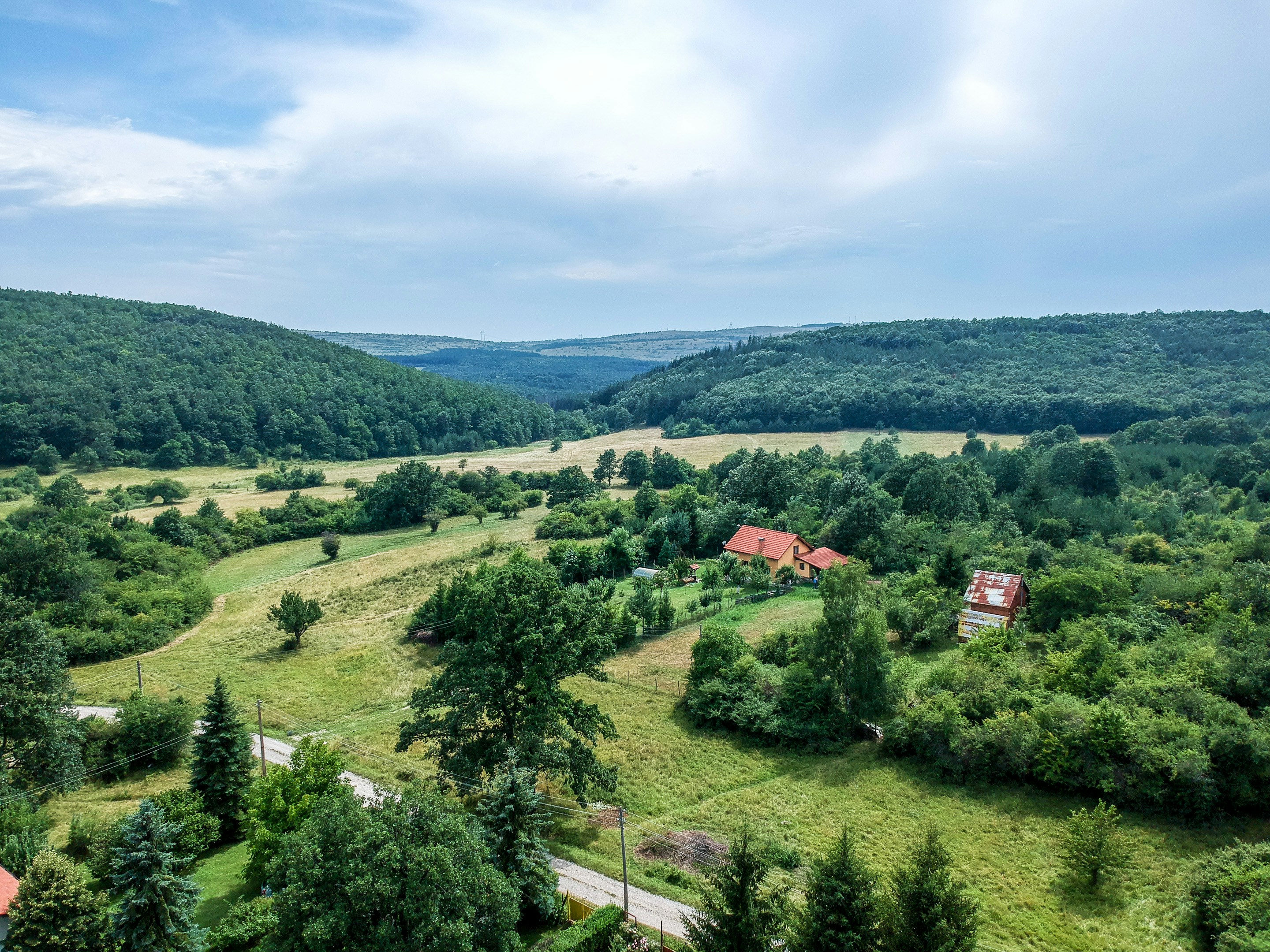Lush green hills and scattered red-roofed houses under a clear blue sky.