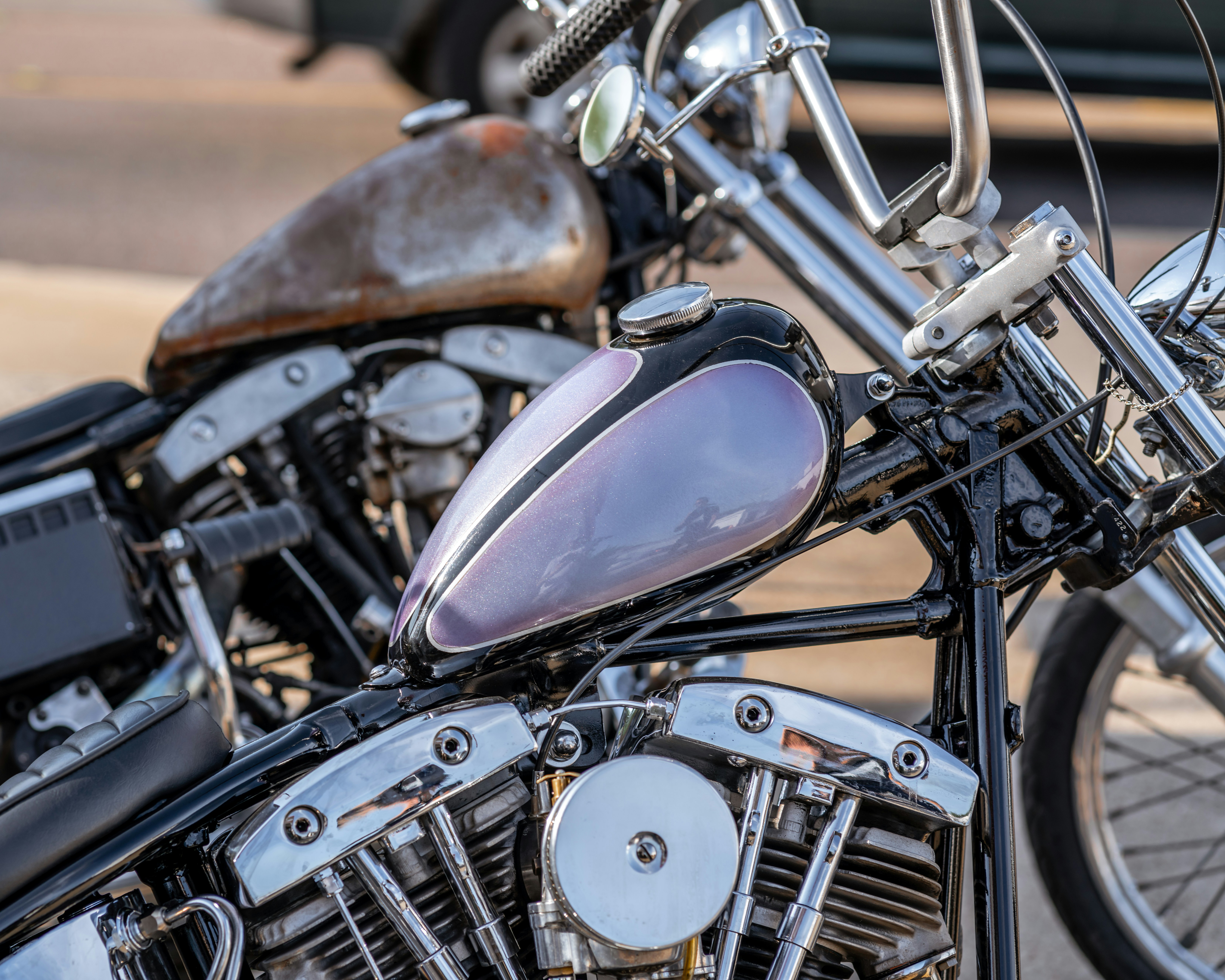 Close-up of two vintage motorcycles showcasing intricate details and contrasting finishes. The polished tank reflects the surrounding environment.