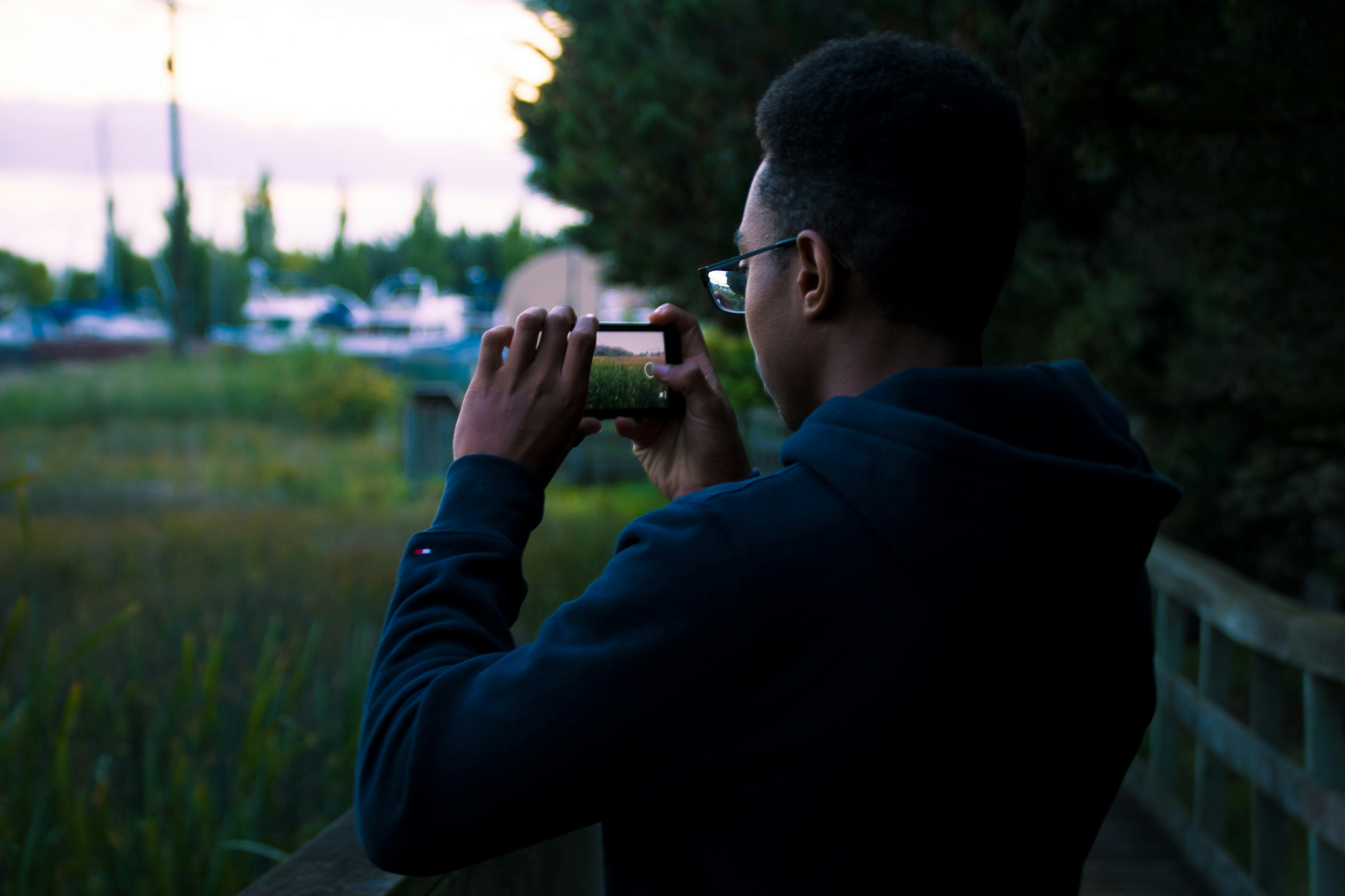Person in a blue hoodie sipping from a glass against a serene evening backdrop.