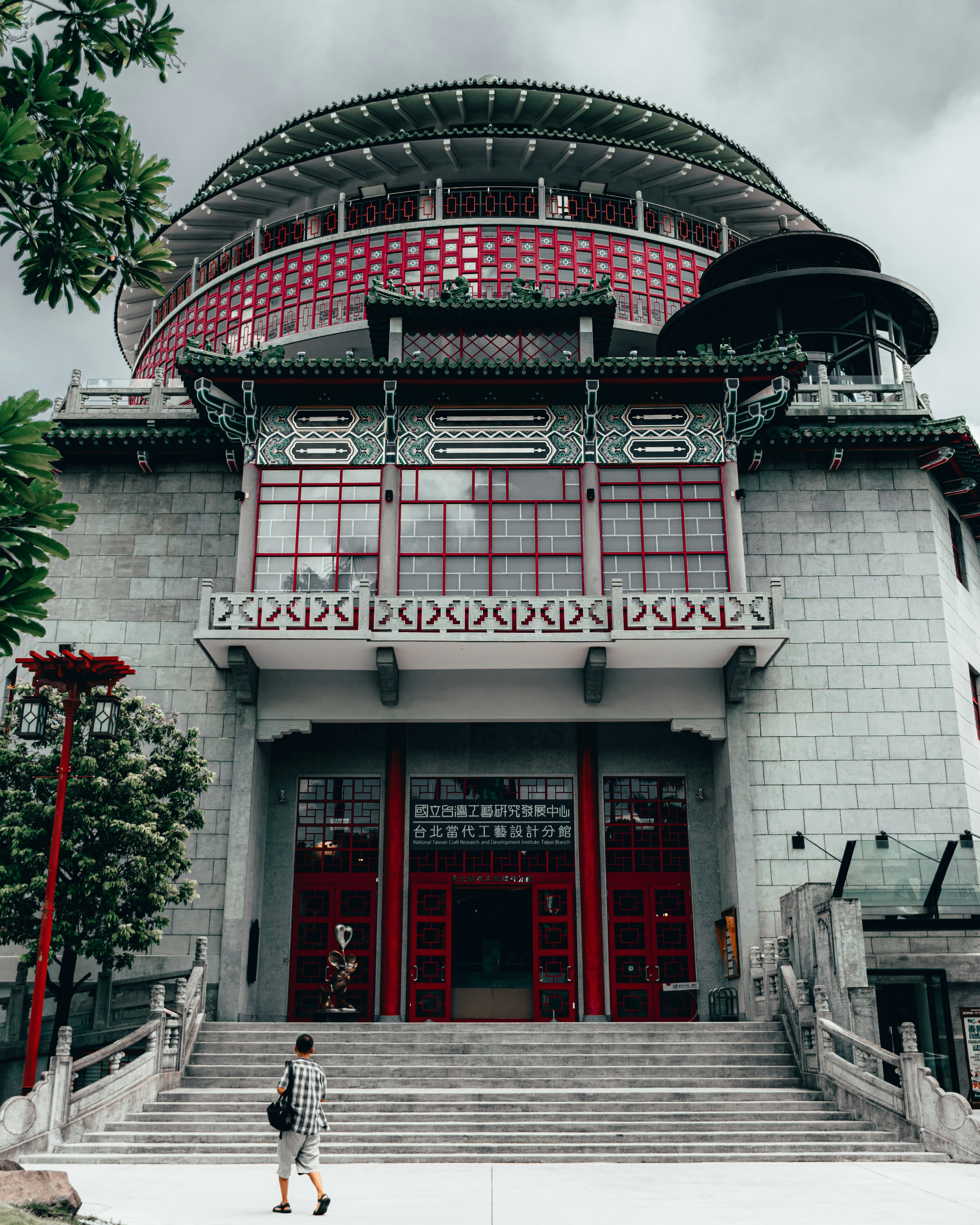 Architectural marvel featuring a blend of traditional and contemporary design elements, with striking red accents and intricate details. A person approaches the grand entrance.