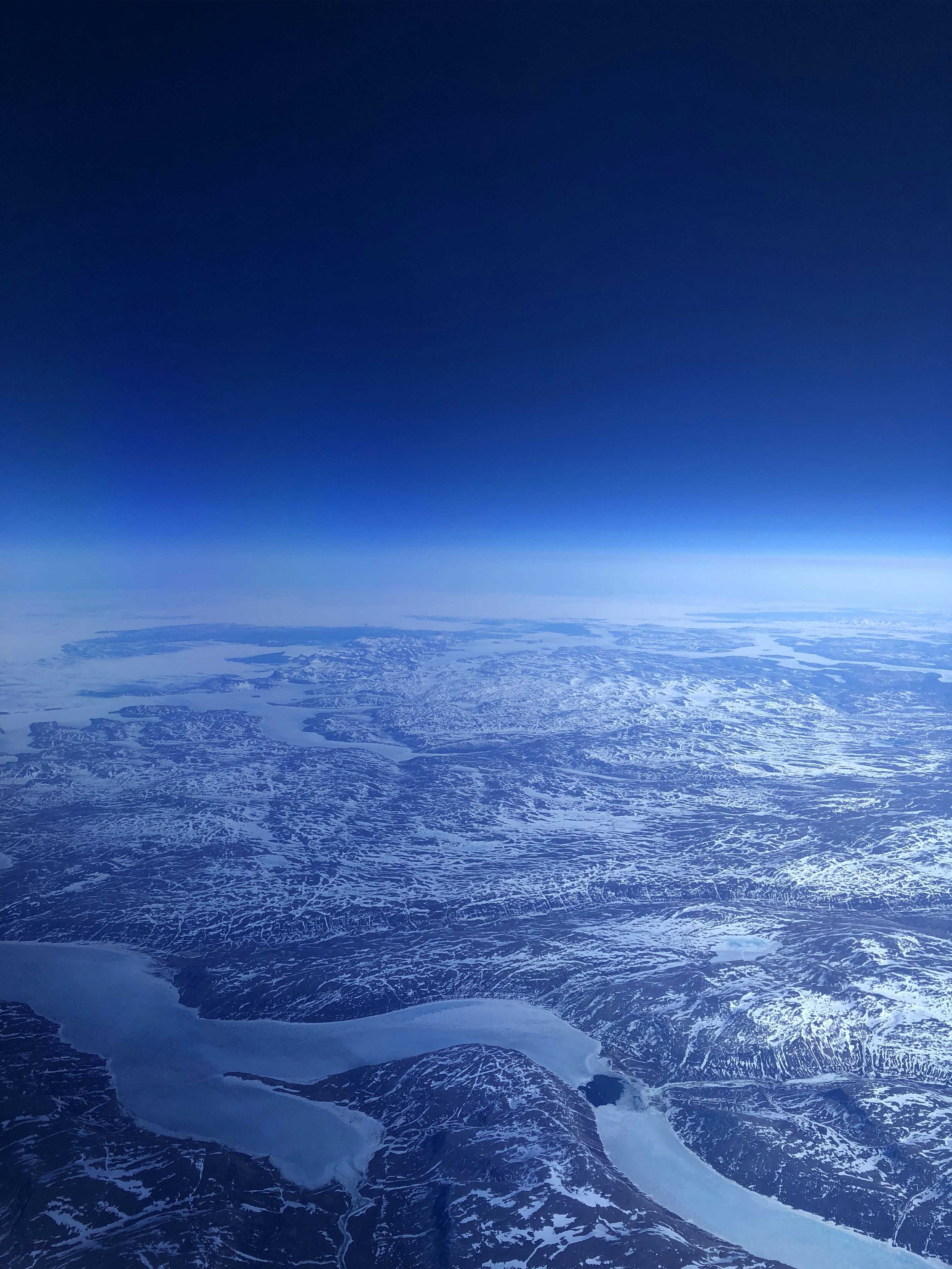 Aerial view of snow-covered terrain and winding rivers under a vast blue sky, showcasing the stark beauty of winter landscapes.