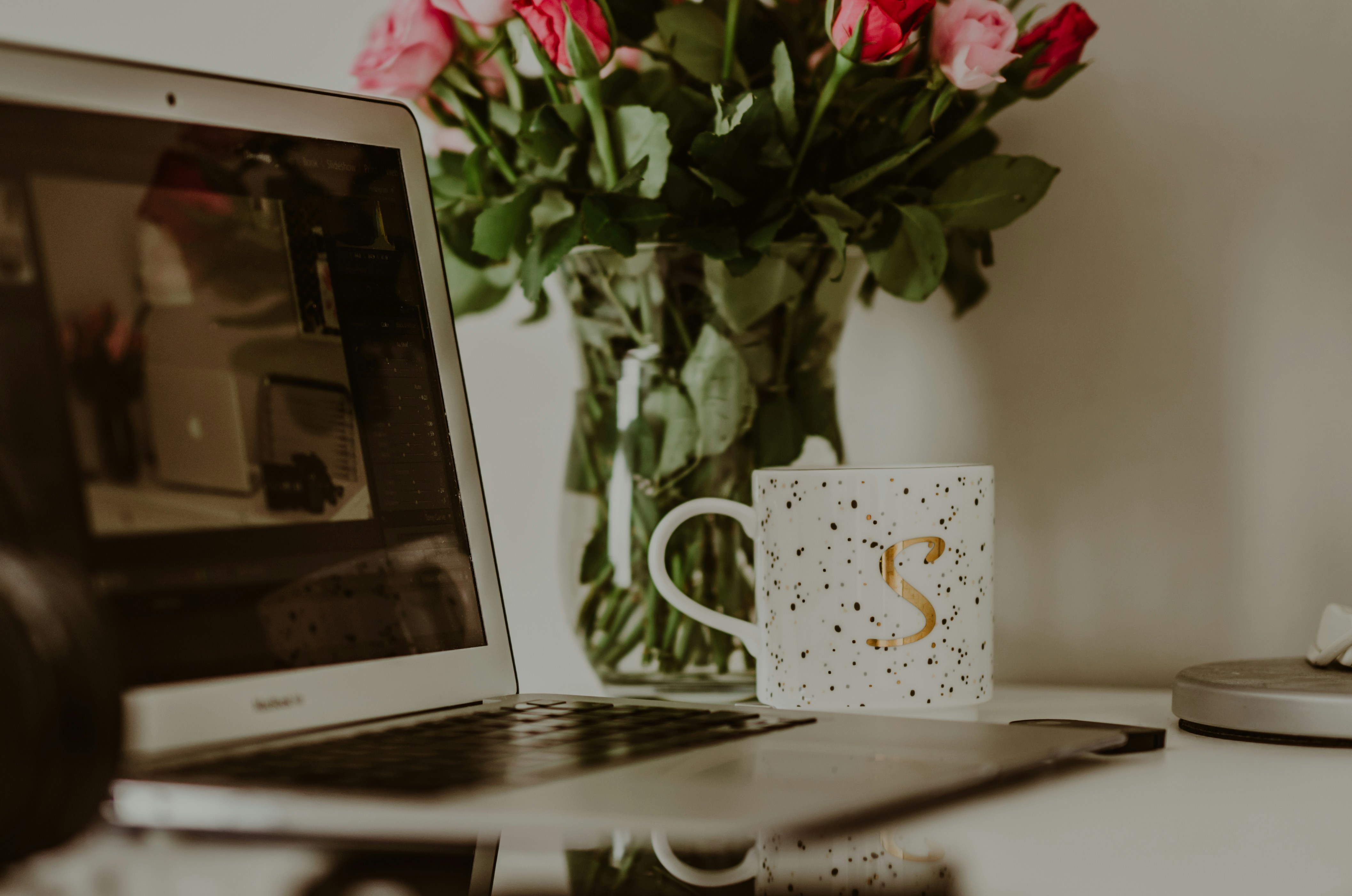 A stylish workspace featuring a laptop, a personalized mug, and a vase of fresh roses, creating an inviting atmosphere for productivity.