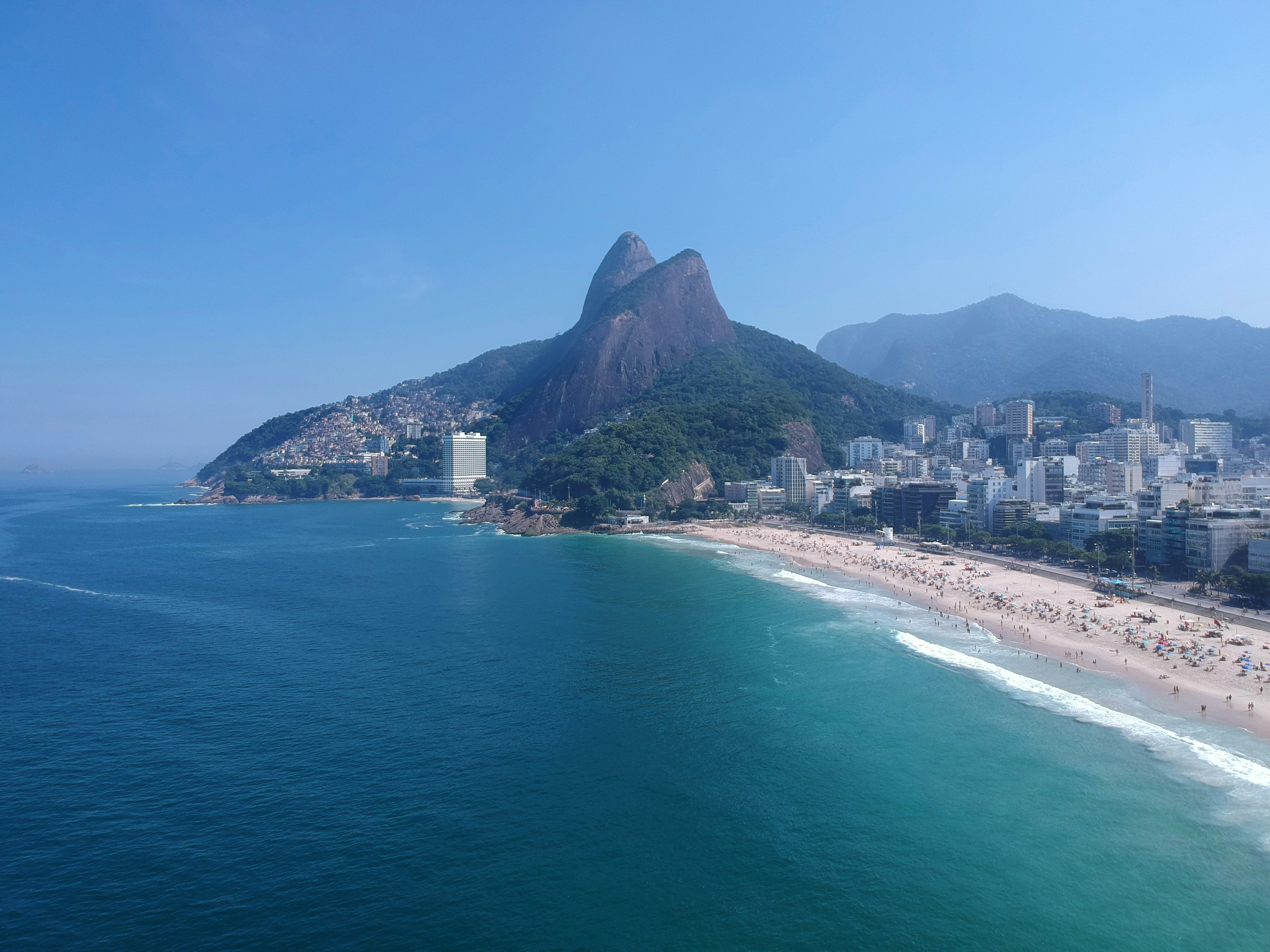 Coastal cityscape with lush mountains meeting the azure ocean under a clear sky.