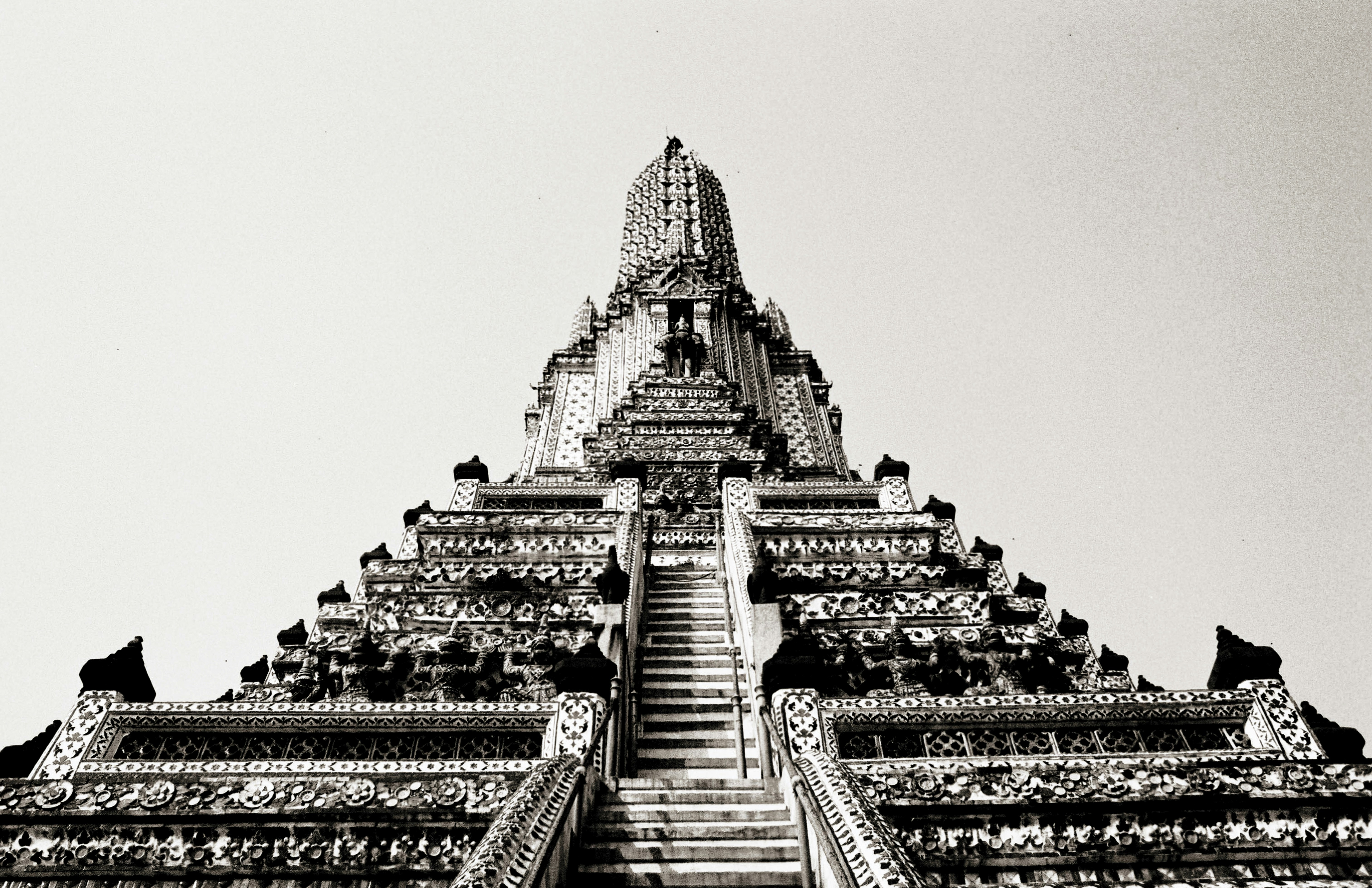 Intricate temple structure viewed from below, showcasing detailed carvings and a steep ascent towards the pinnacle.