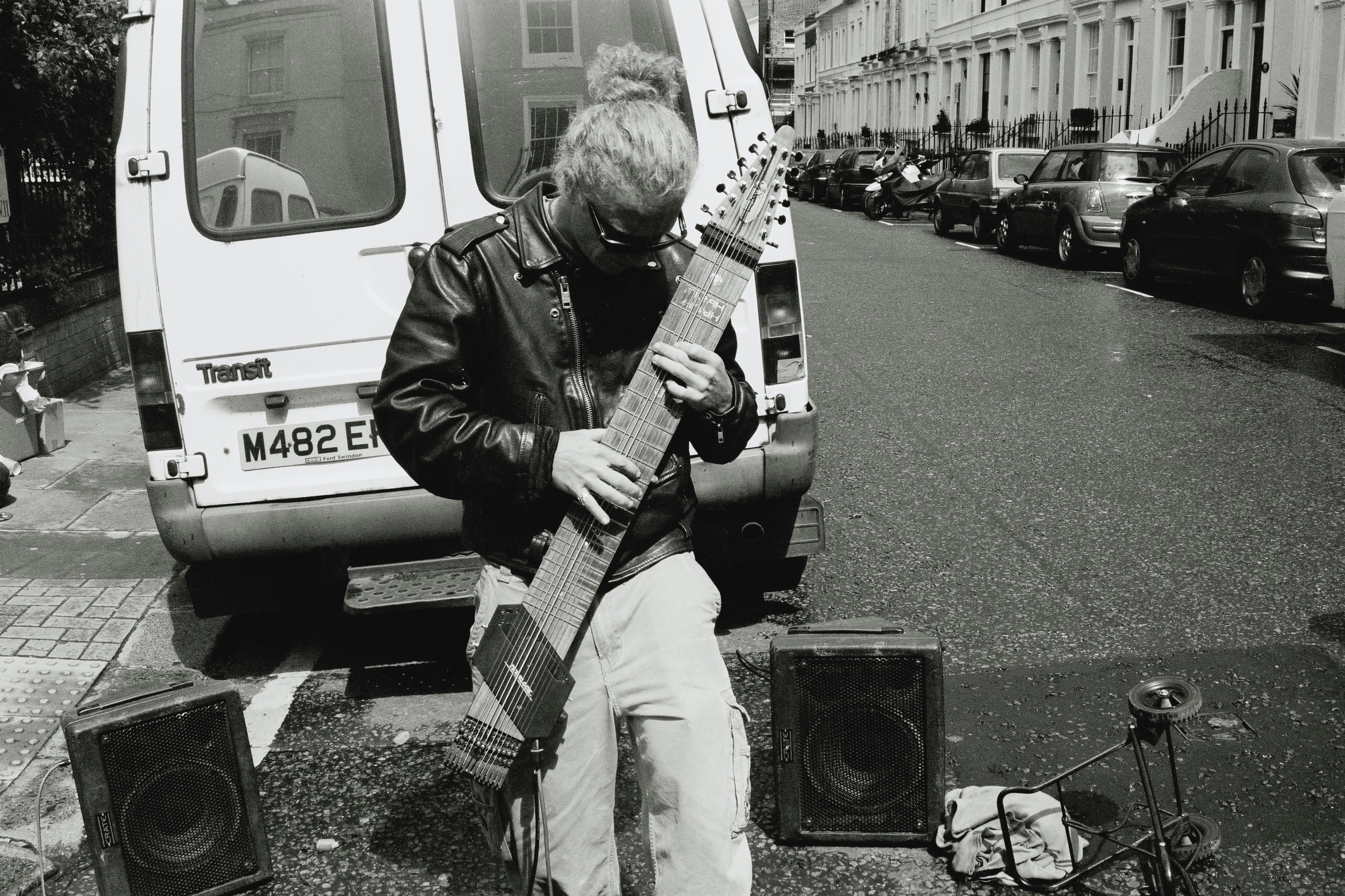 Curbside Resonance: A street musician commands a long, guitar-like instrument among parked vans