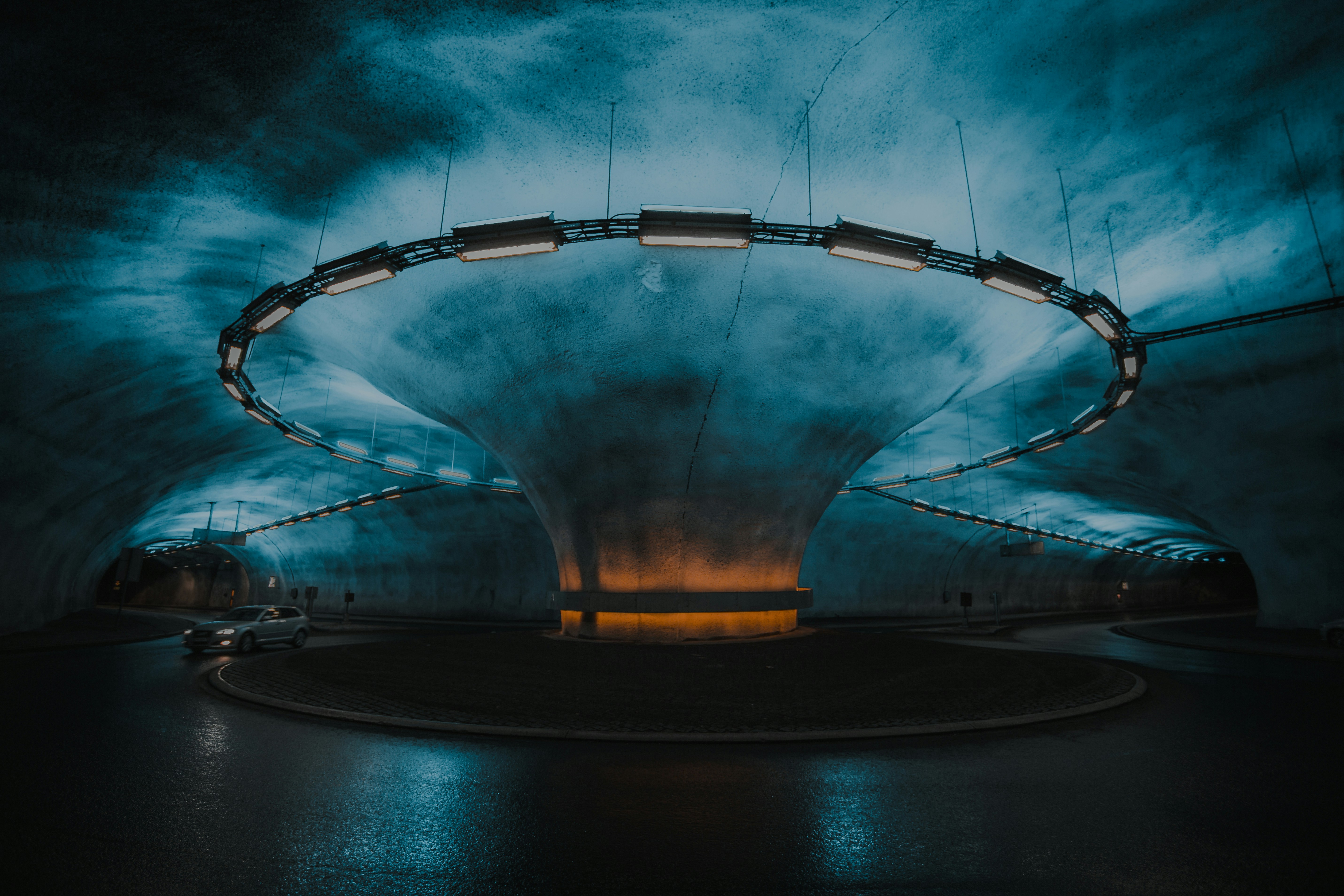 Illuminated circular structure in a tunnel, casting a soft glow on the wet pavement below. The interplay of light and shadow creates a surreal atmosphere.