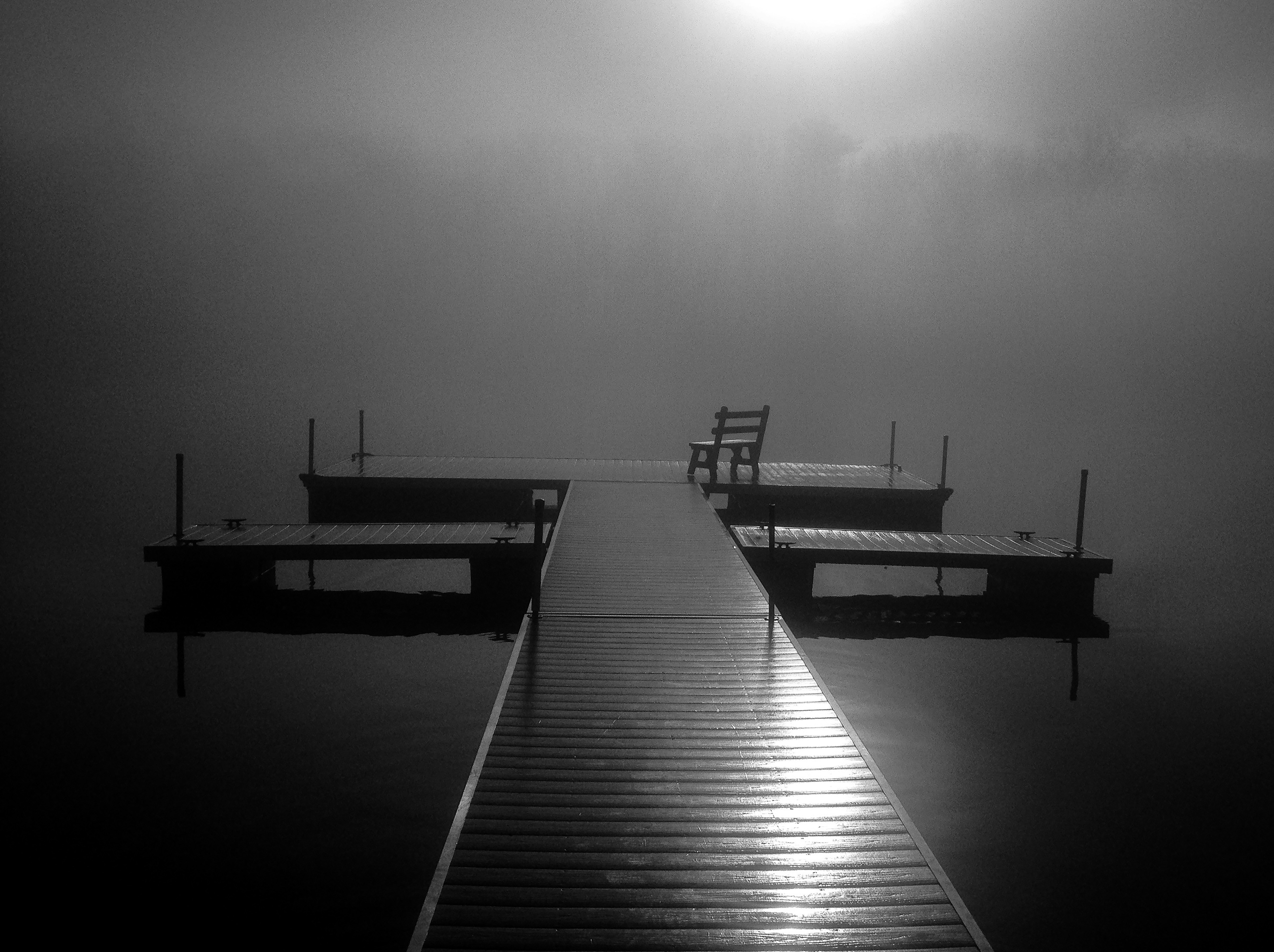 Lonely dock with a solitary bench shrouded in morning fog, reflecting on still waters.