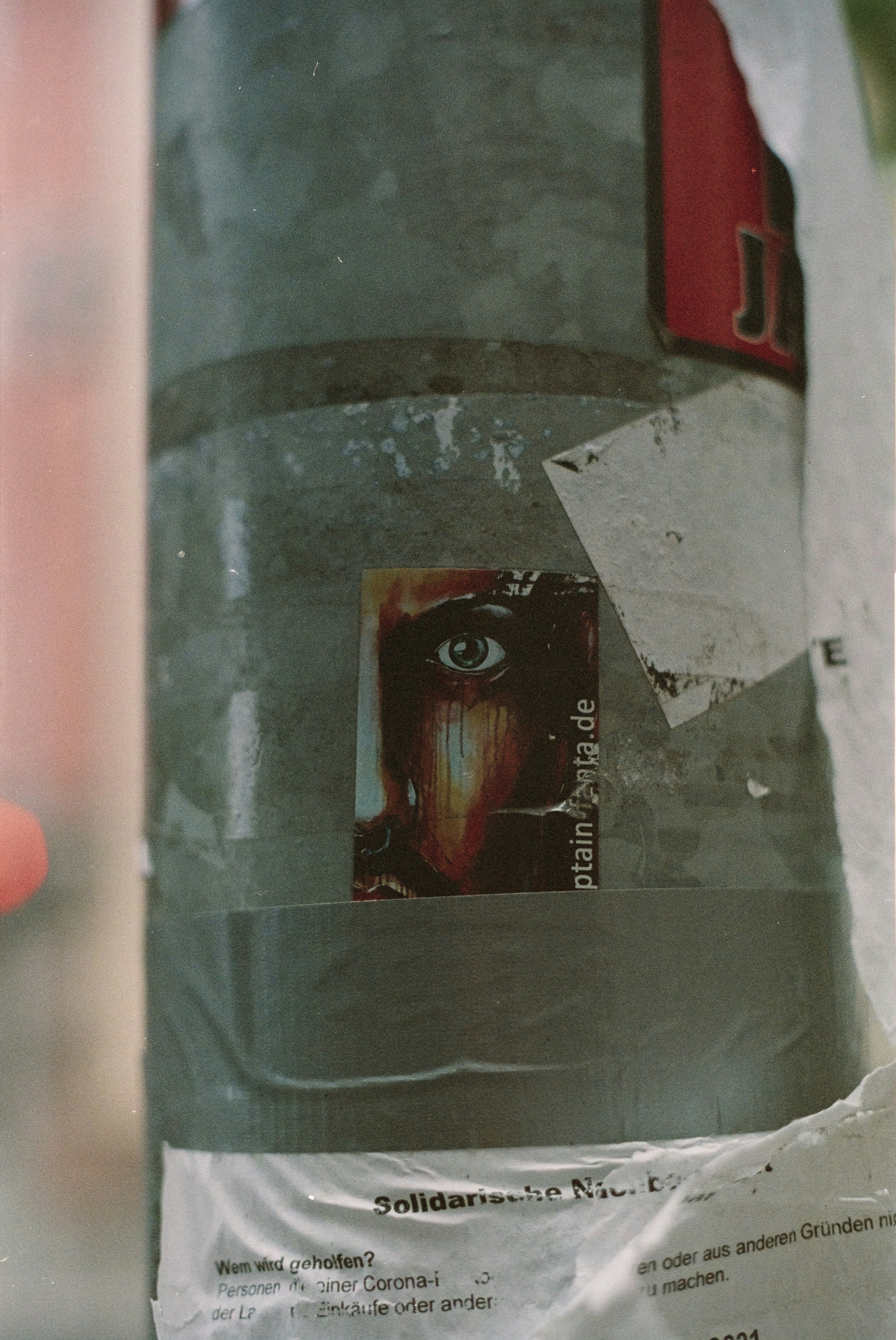 A partially torn poster revealing a striking eye and face amidst layers of urban decay and graffiti. The image captures the essence of street art and its interaction with the environment.