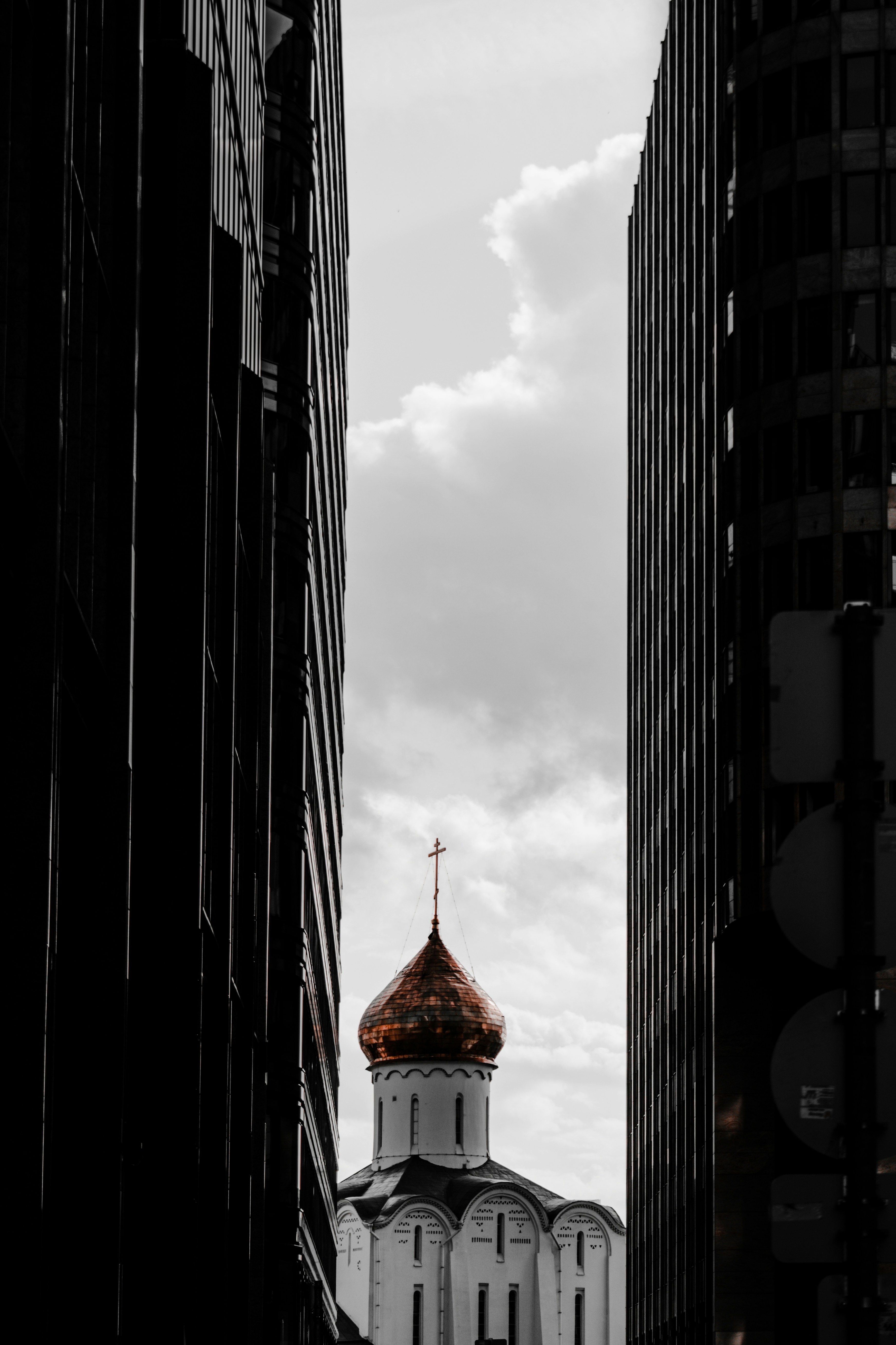 A golden-domed church peeks through a narrow alley flanked by towering skyscrapers, showcasing the juxtaposition of old and new architecture.