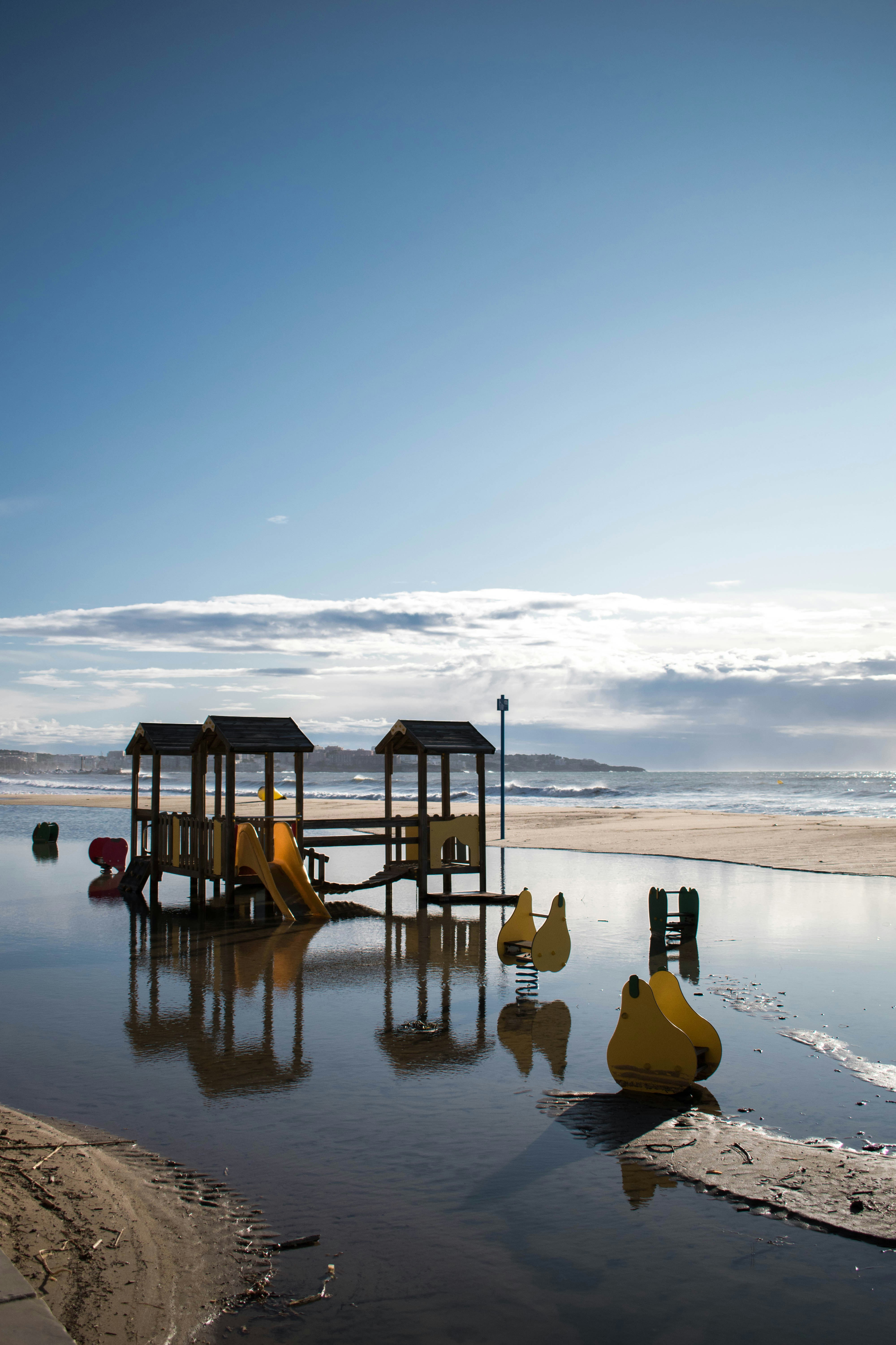 Submerged Playground: Wooden Towers and Yellow Slides Reflect in Tidal Glass