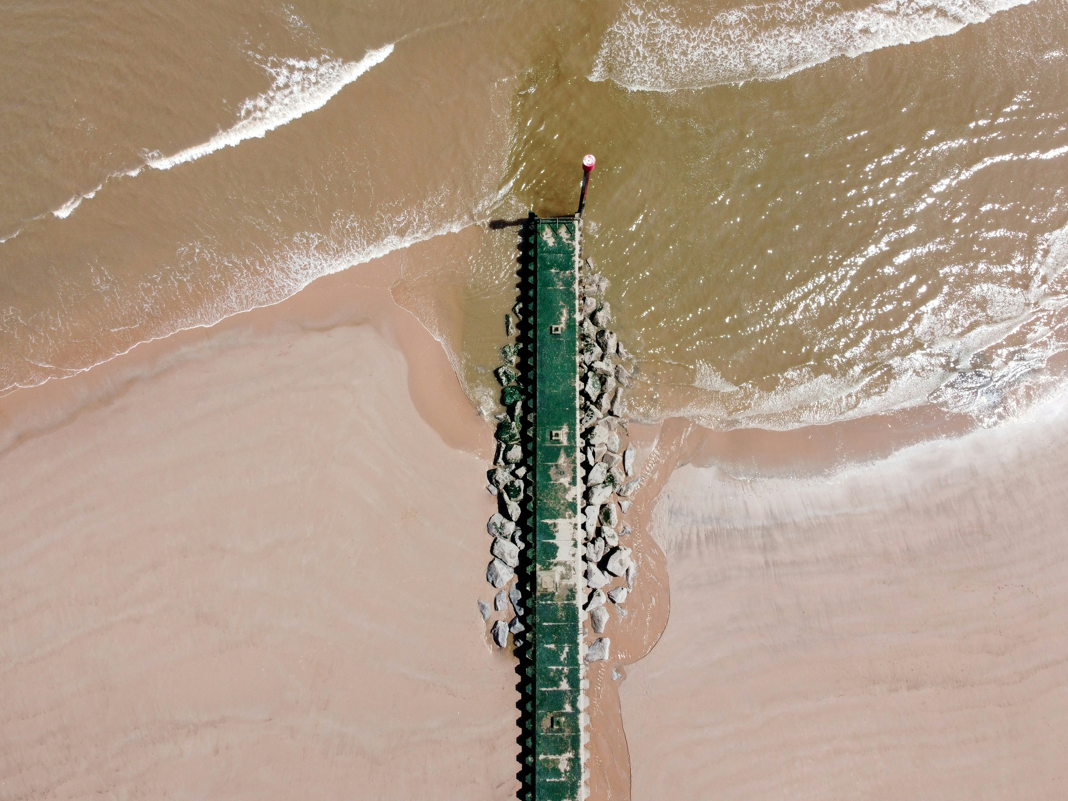 Green-Deck Jetty Cuts a Quiet Path Through a Pink-Sand Shore