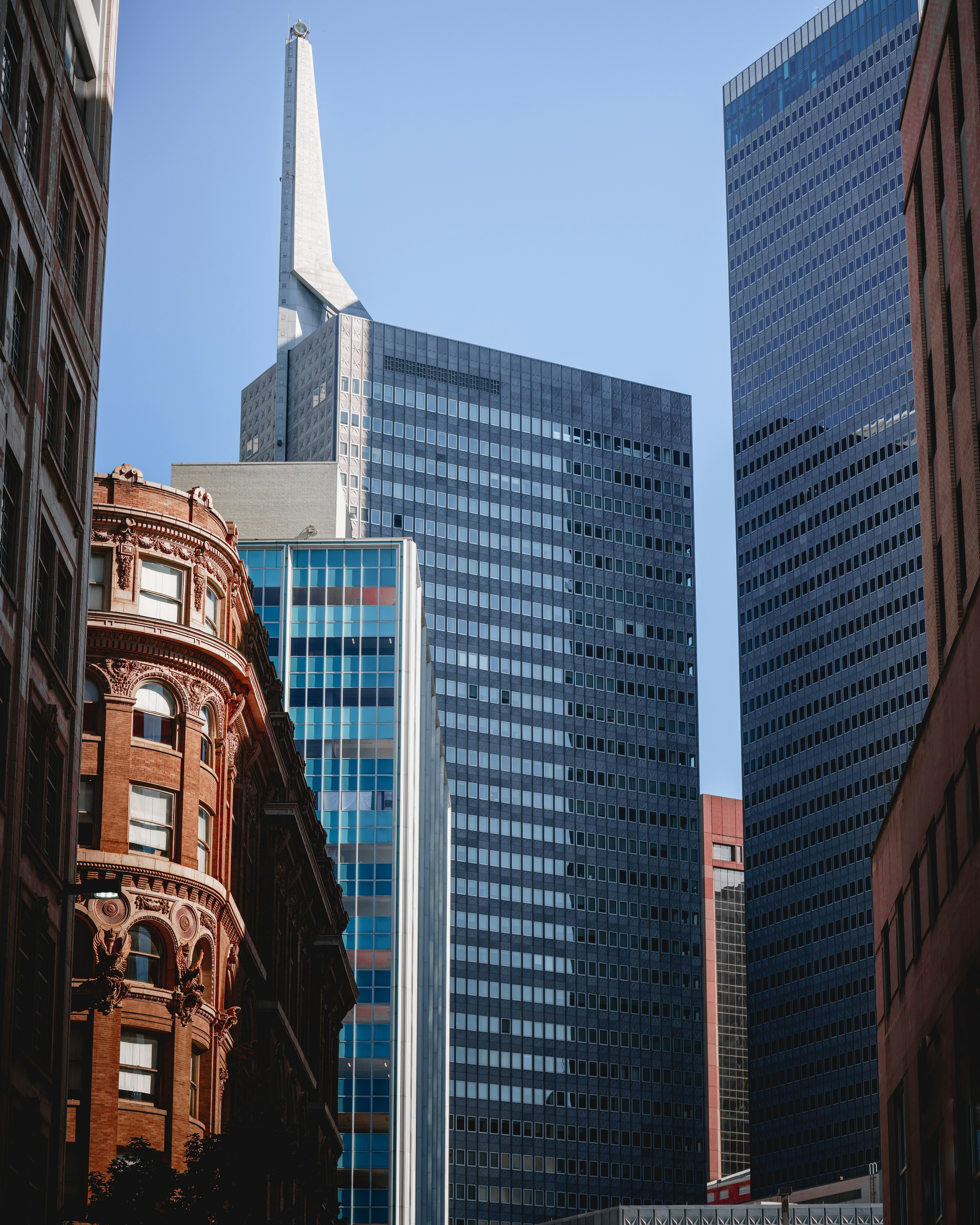 Historic red brick building juxtaposed with sleek modern skyscrapers under a clear blue sky.