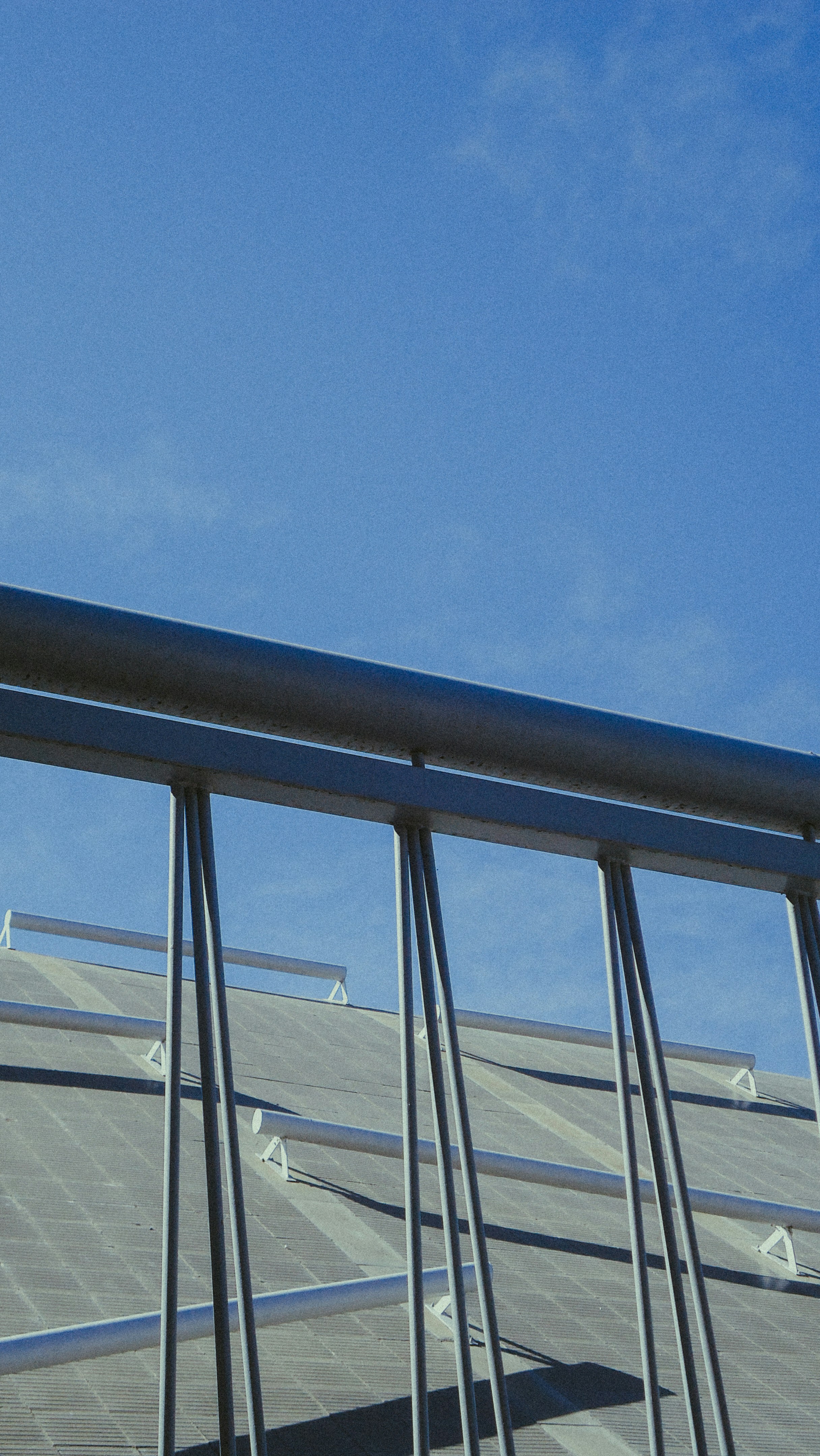 Blue sky backdrop with metal railing lines over a solar-panel roof, highlighting geometric structure.
