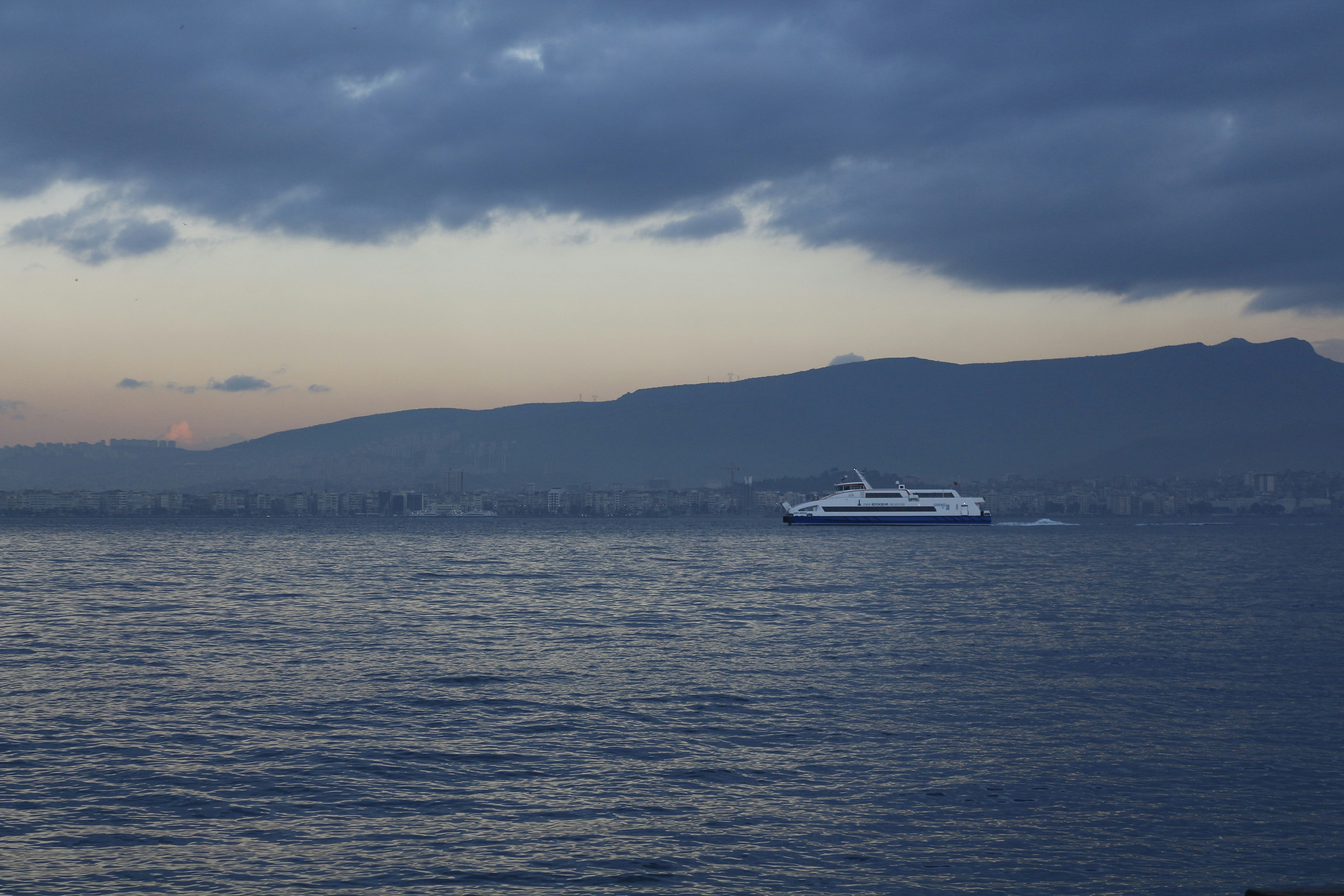 Ferry glides across a tranquil sea under a cloudy twilight sky.