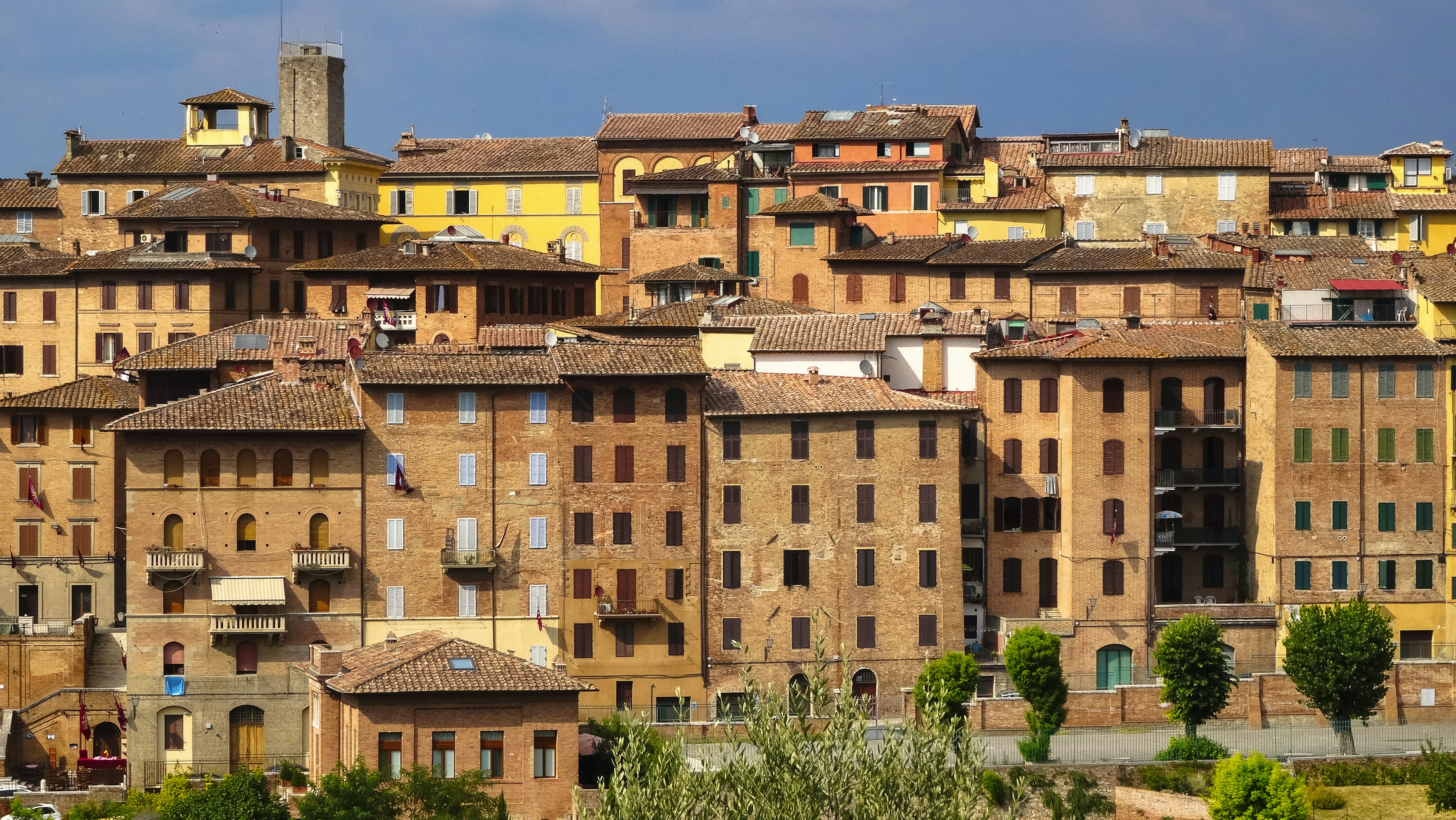 Historic buildings with terracotta facades nestled against a dramatic sky in Siena, Italy.