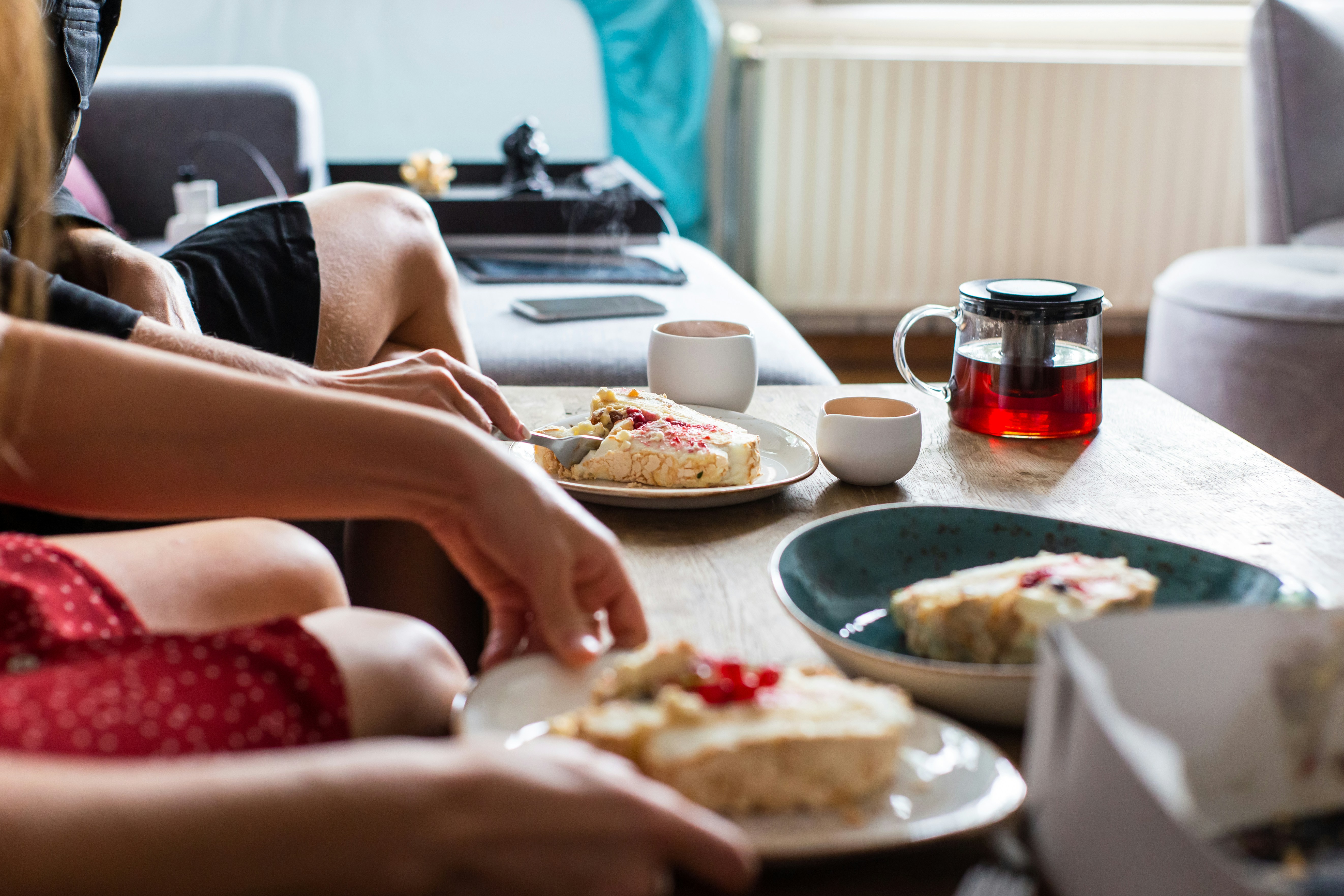 Hands reaching for dessert on a coffee table set with tea and pastries.