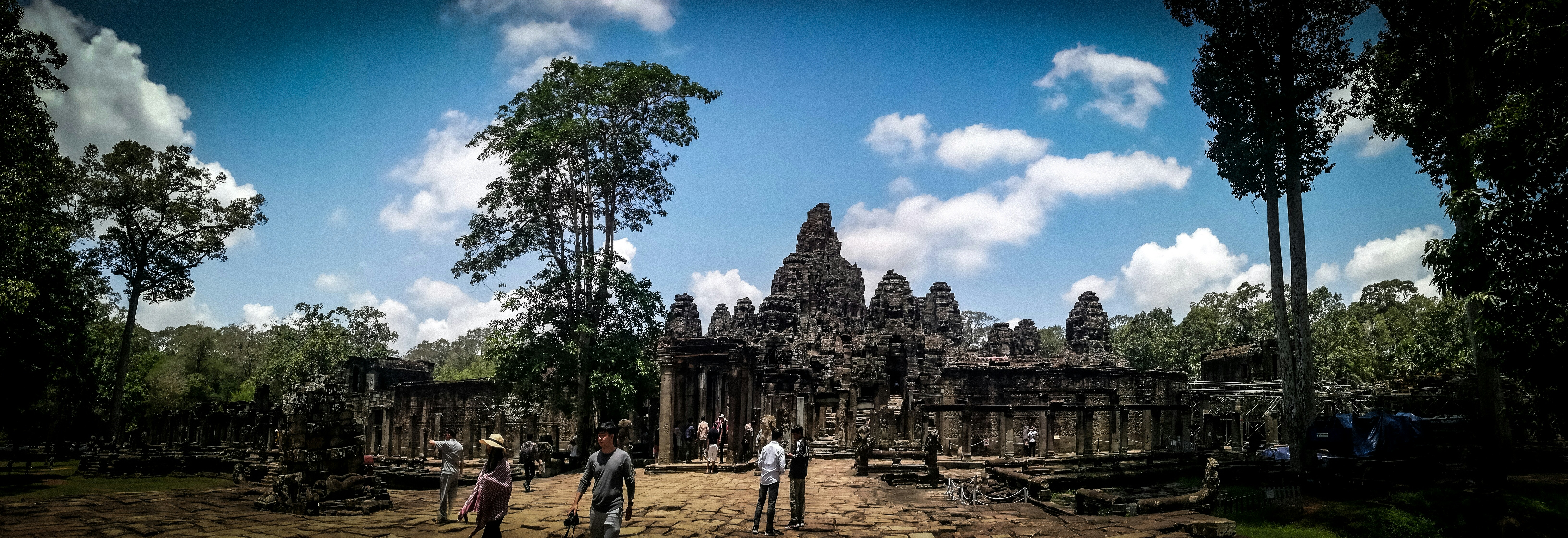 Majestic temple ruins surrounded by lush trees and a bright blue sky, with visitors exploring the historic site.