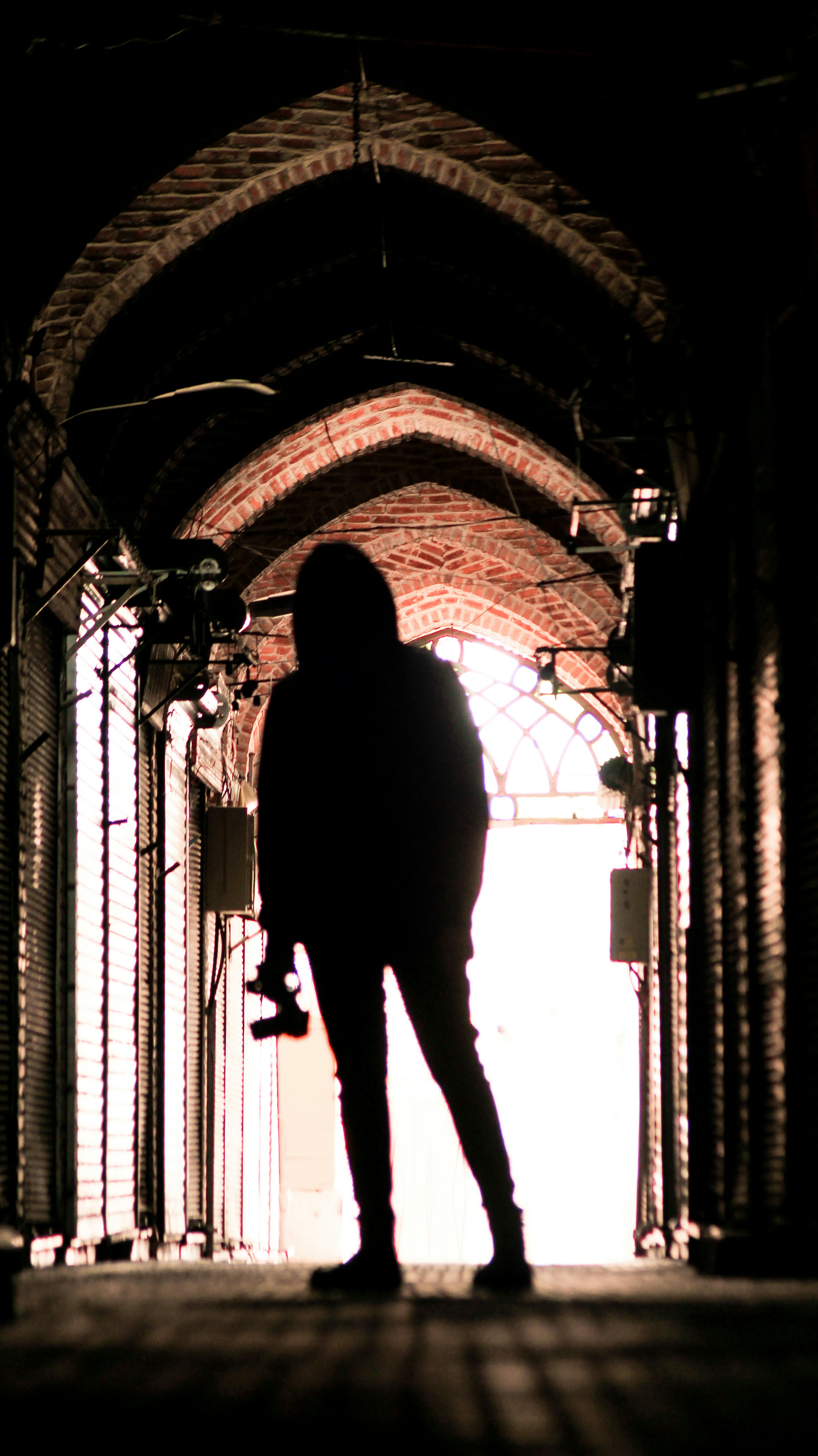 Shadow at the Arch: A Lone Figure in a Brick-Vaulted Corridor