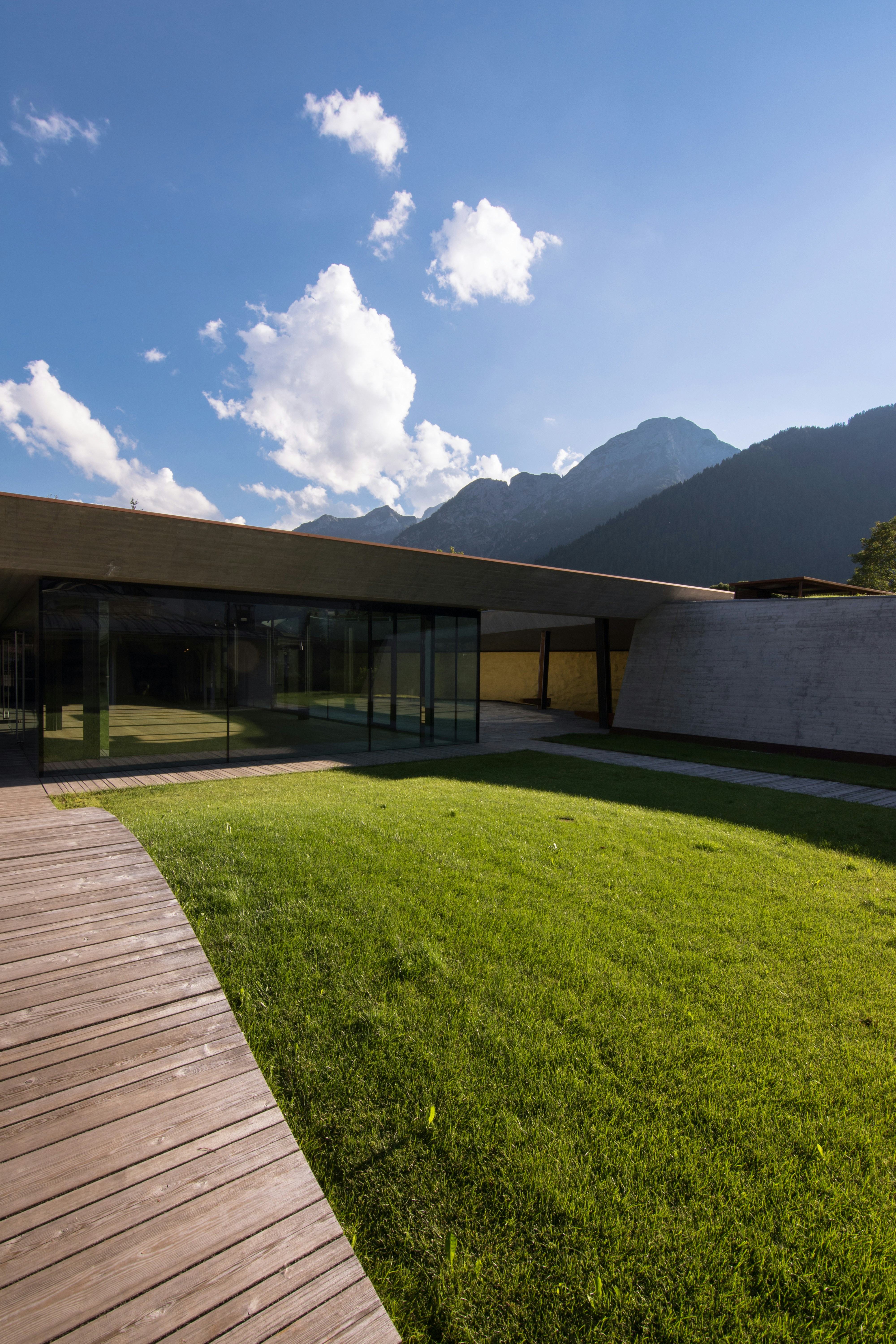 brown wooden house on green grass field near mountain under white clouds during daytime