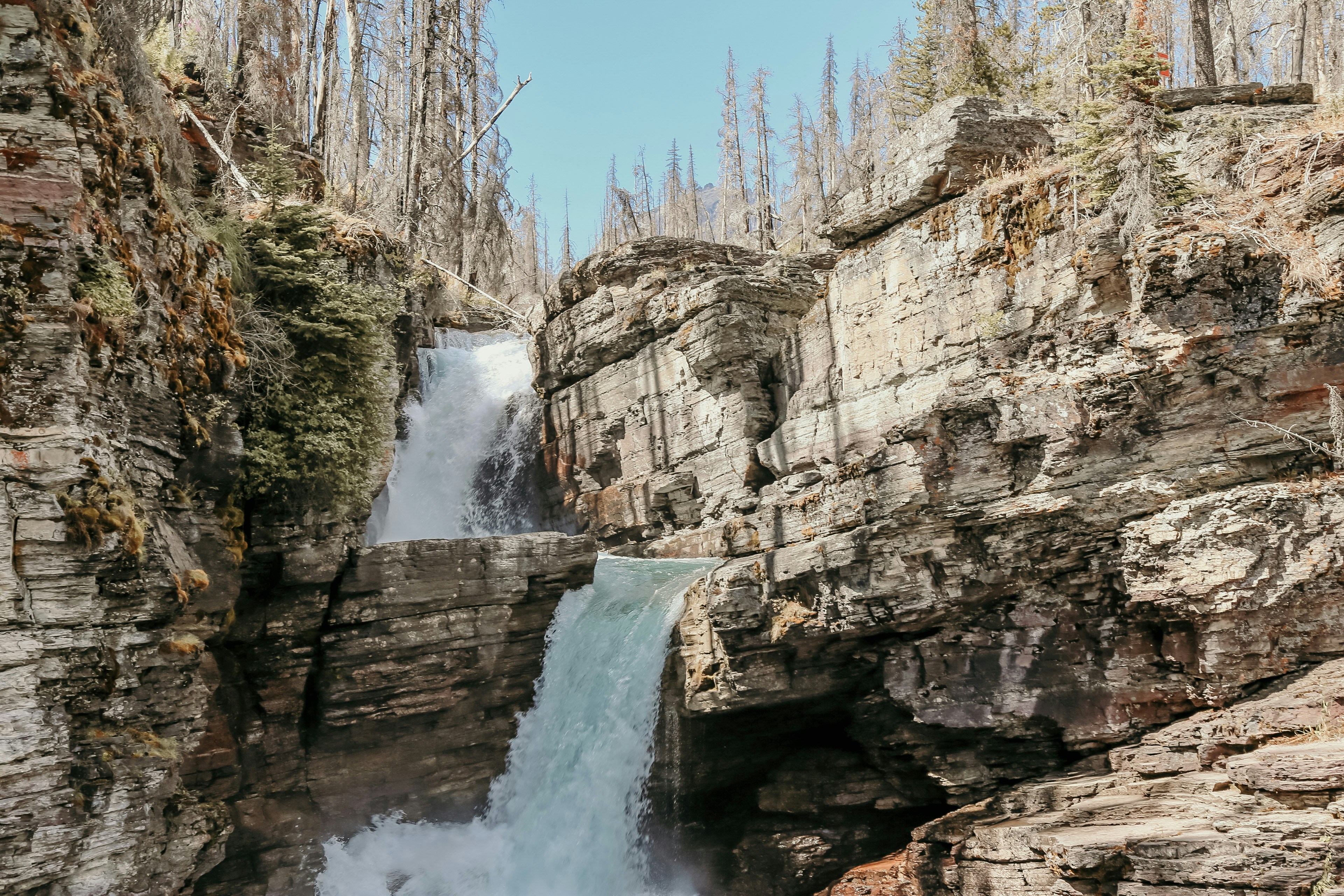 Waterfall cascading through rugged rock formations under a clear blue sky.