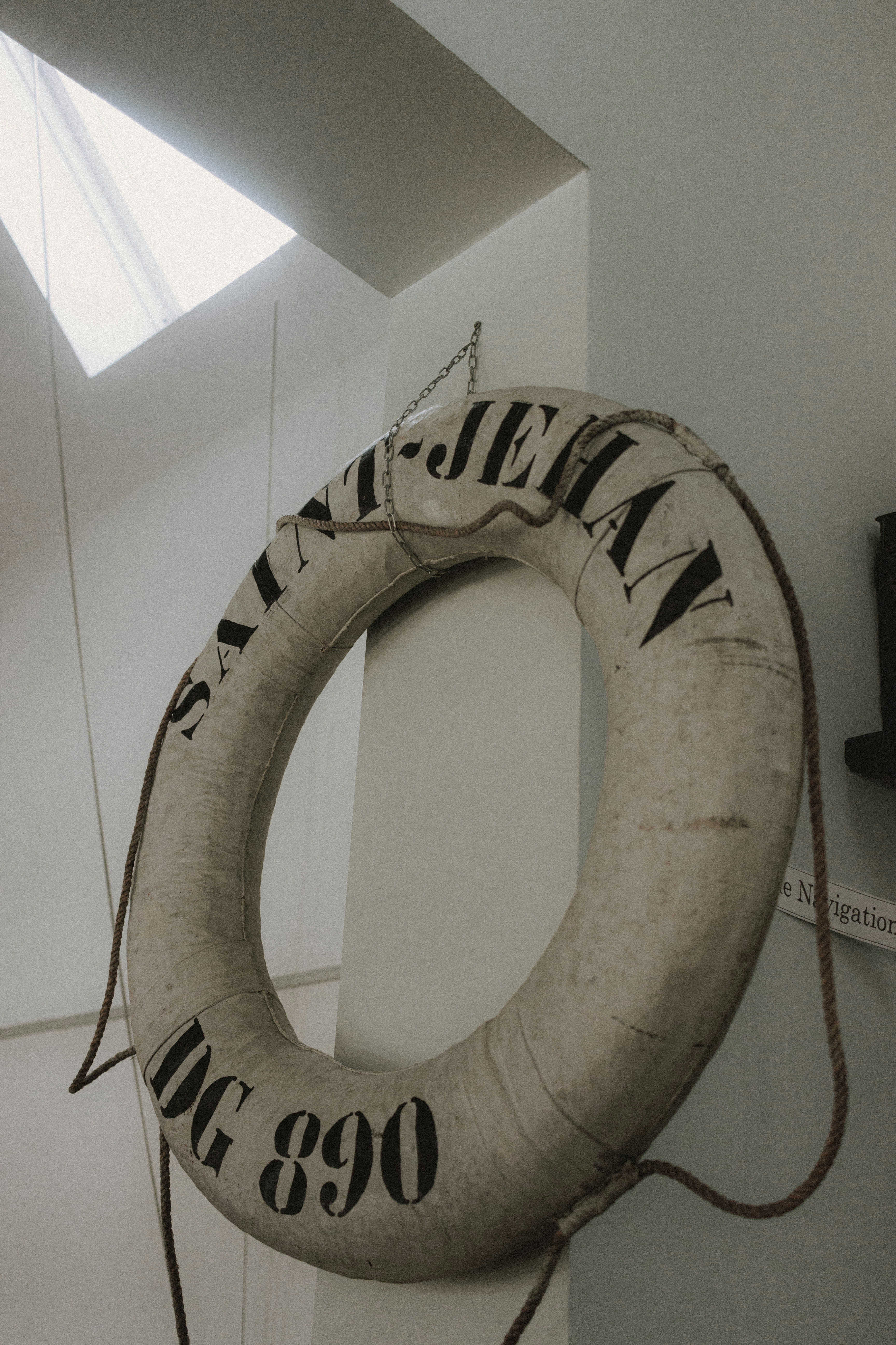 Weathered lifebuoy labeled 'SAINT JEHAN DG 890' hanging against a minimalist background, evoking maritime nostalgia.