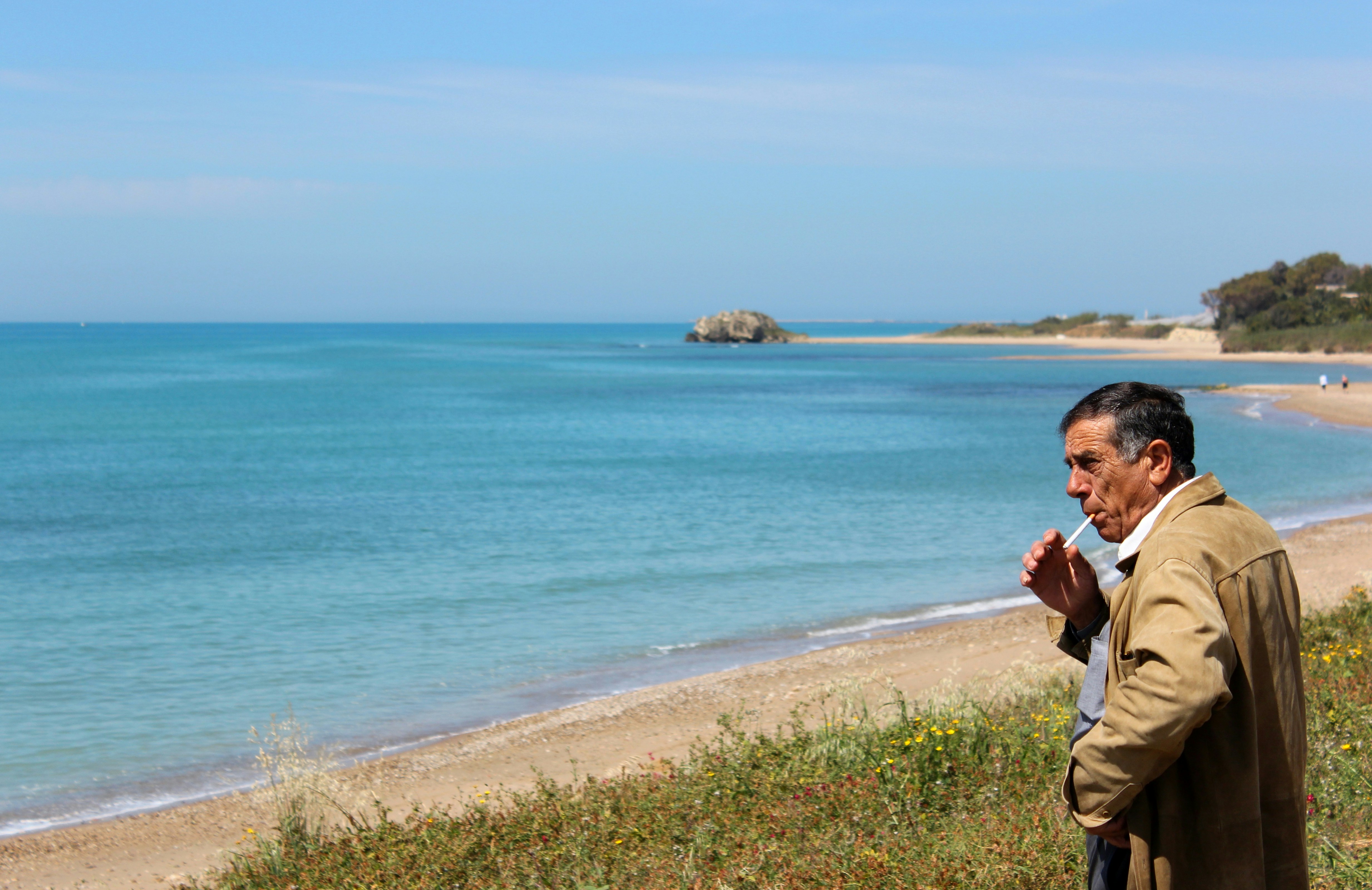 Coastline Interlude: A Man in a Tan Coat Stands by the Quiet Tide.