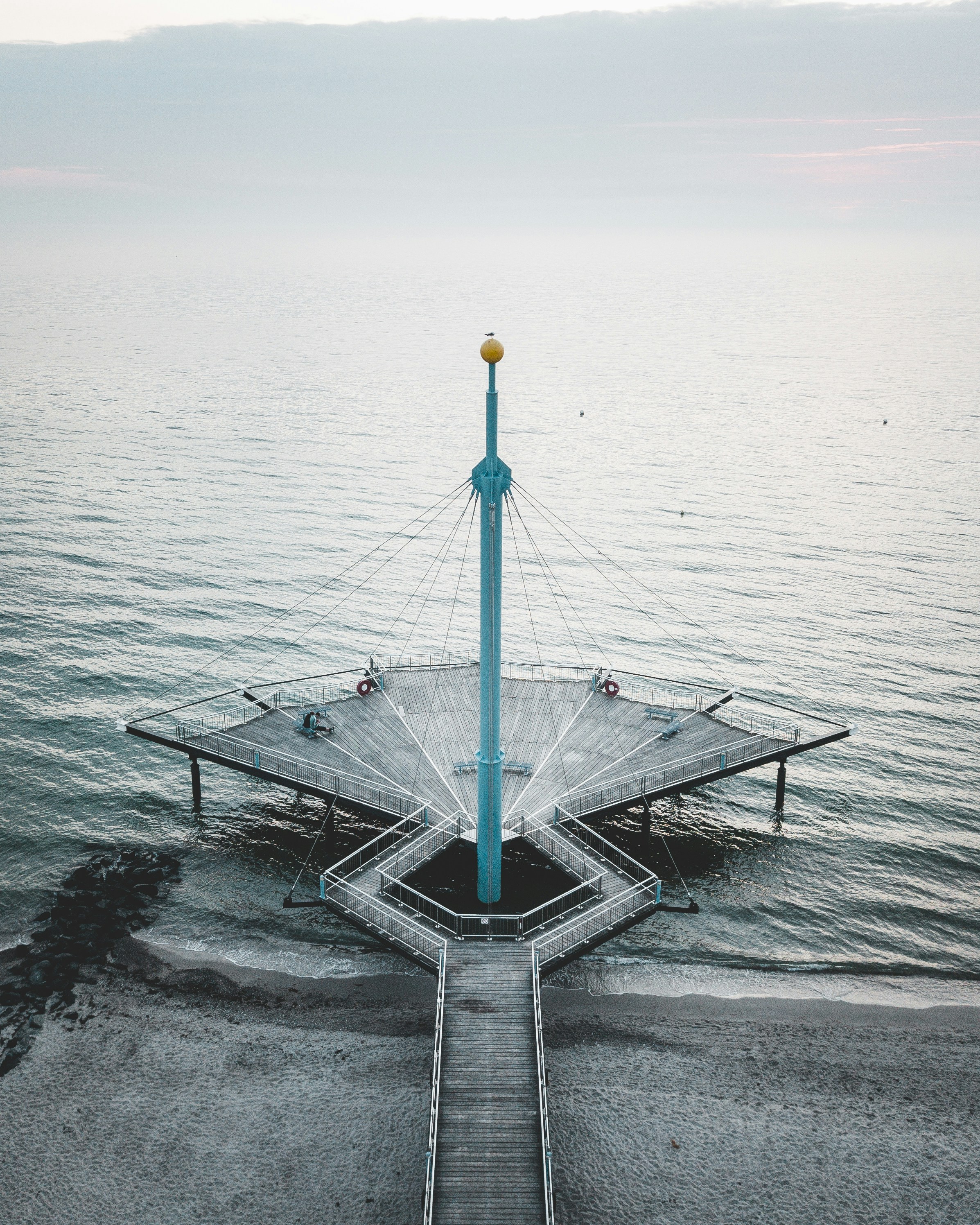Blue Mast at the Center: A Geometric Pier Reaching into the Calm Sea