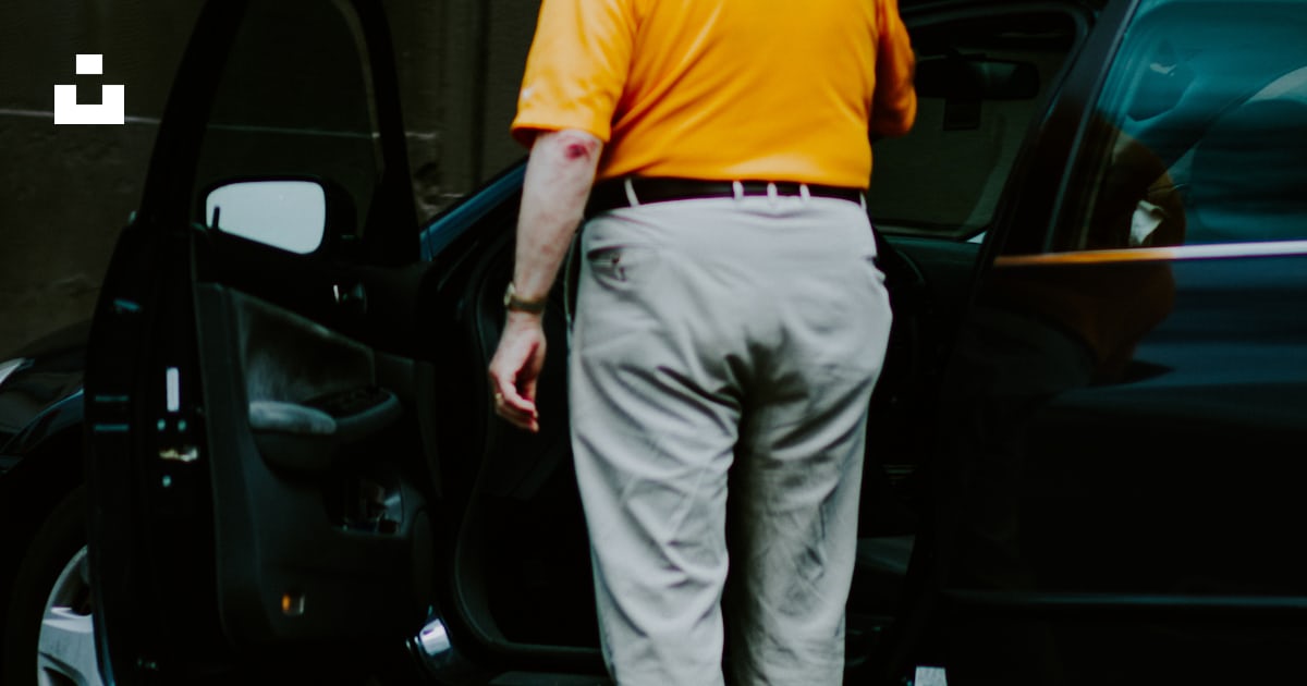 Man In Orange Shirt And Gray Pants Standing Beside Black Car Photo