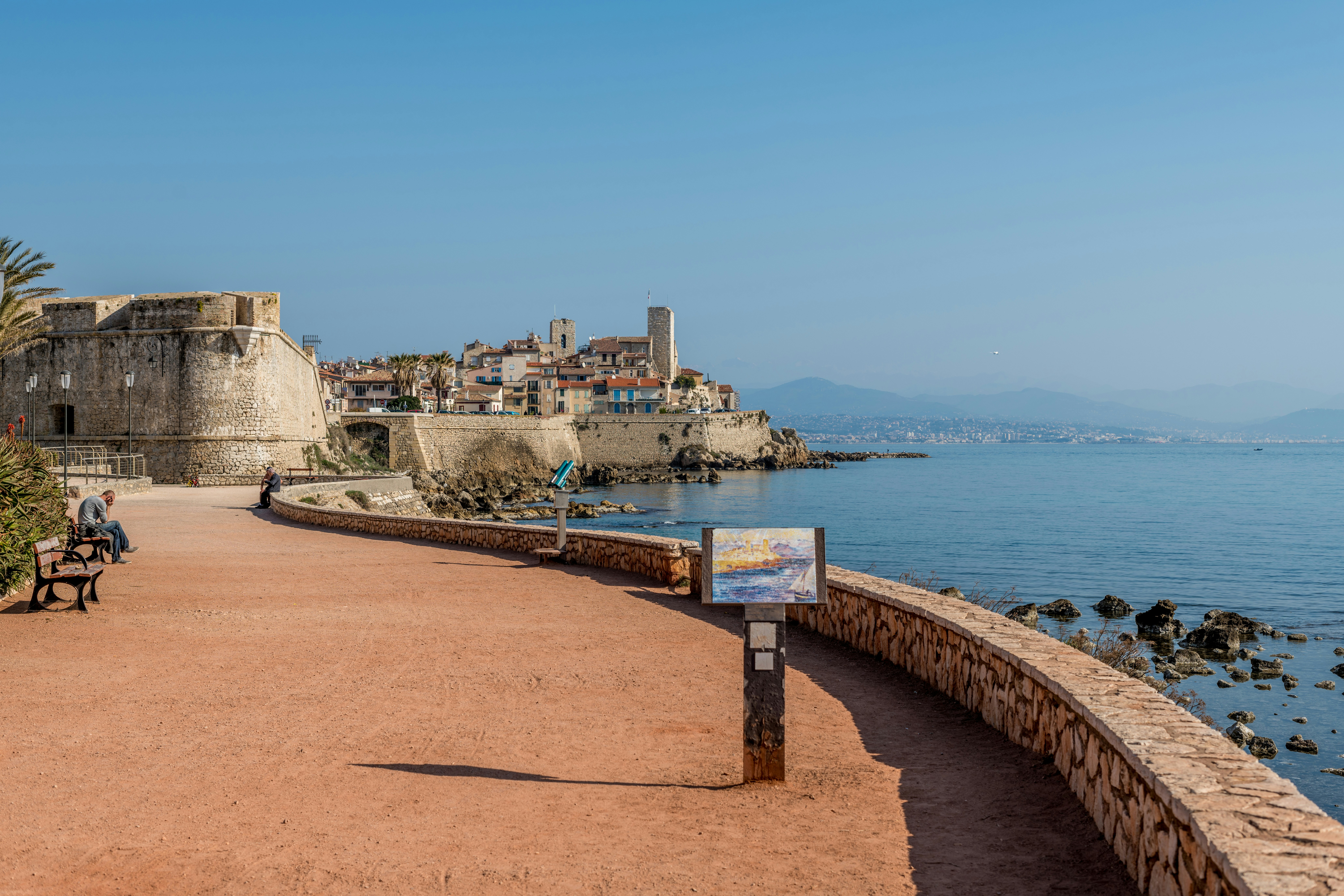 Coastal pathway in Antibes, featuring a historic fort and tranquil waters under a clear blue sky.