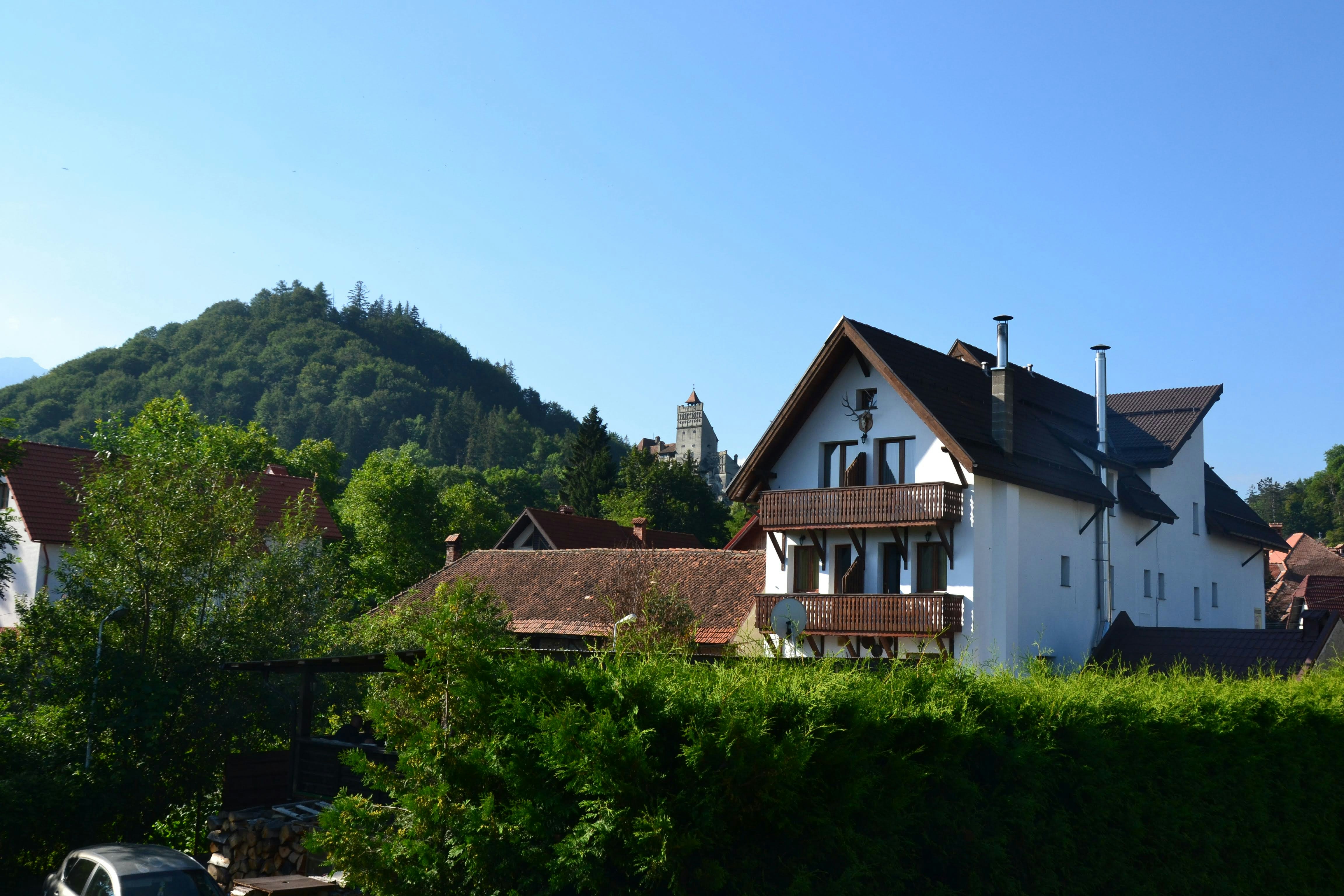 Bran Castle, also known as Dracula's Castle | white and brown house surrounded by green trees under blue sky during daytime