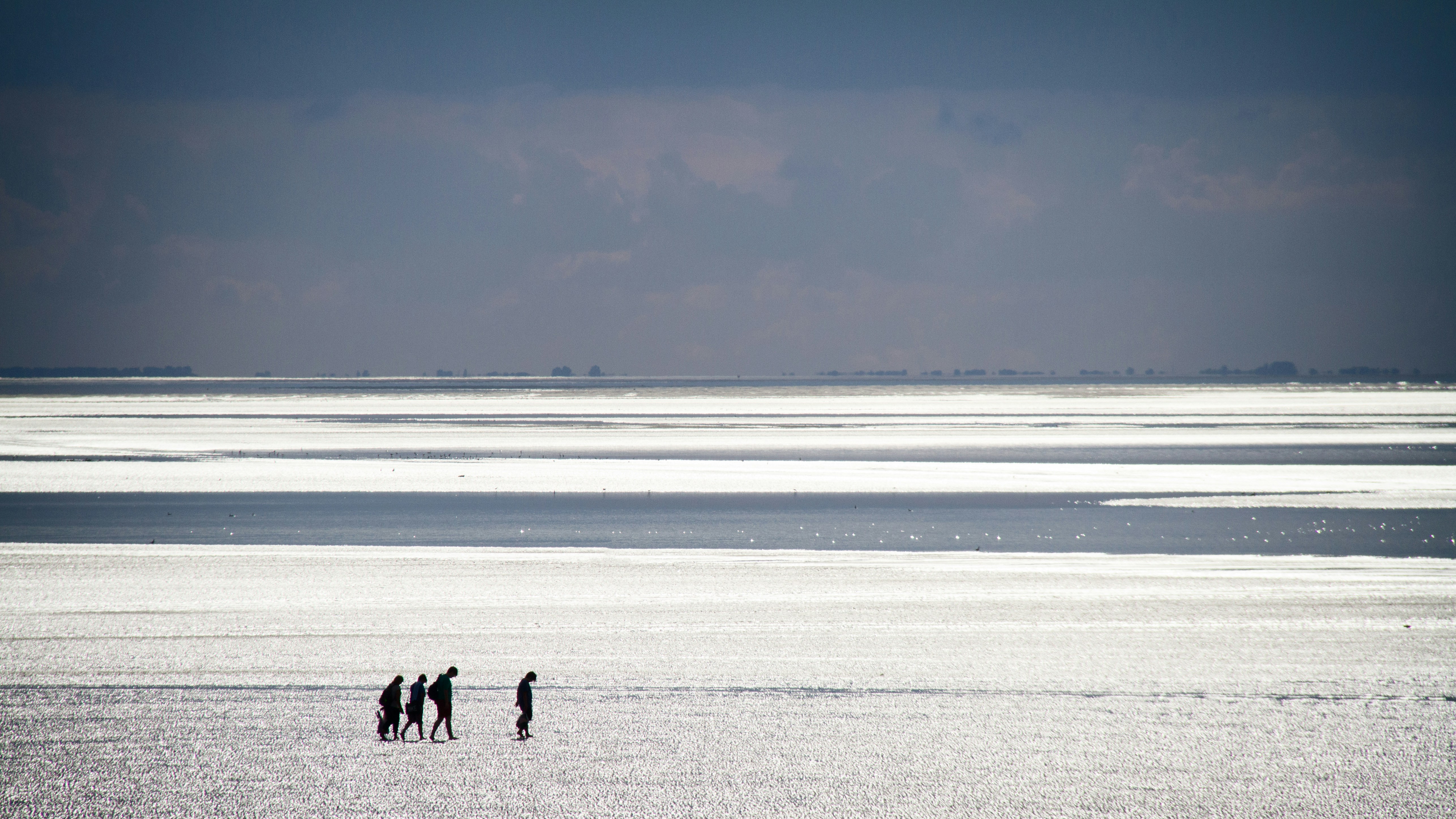 Five Silhouettes Traverse a Quiet Salt Flat Beneath a Moody Sky