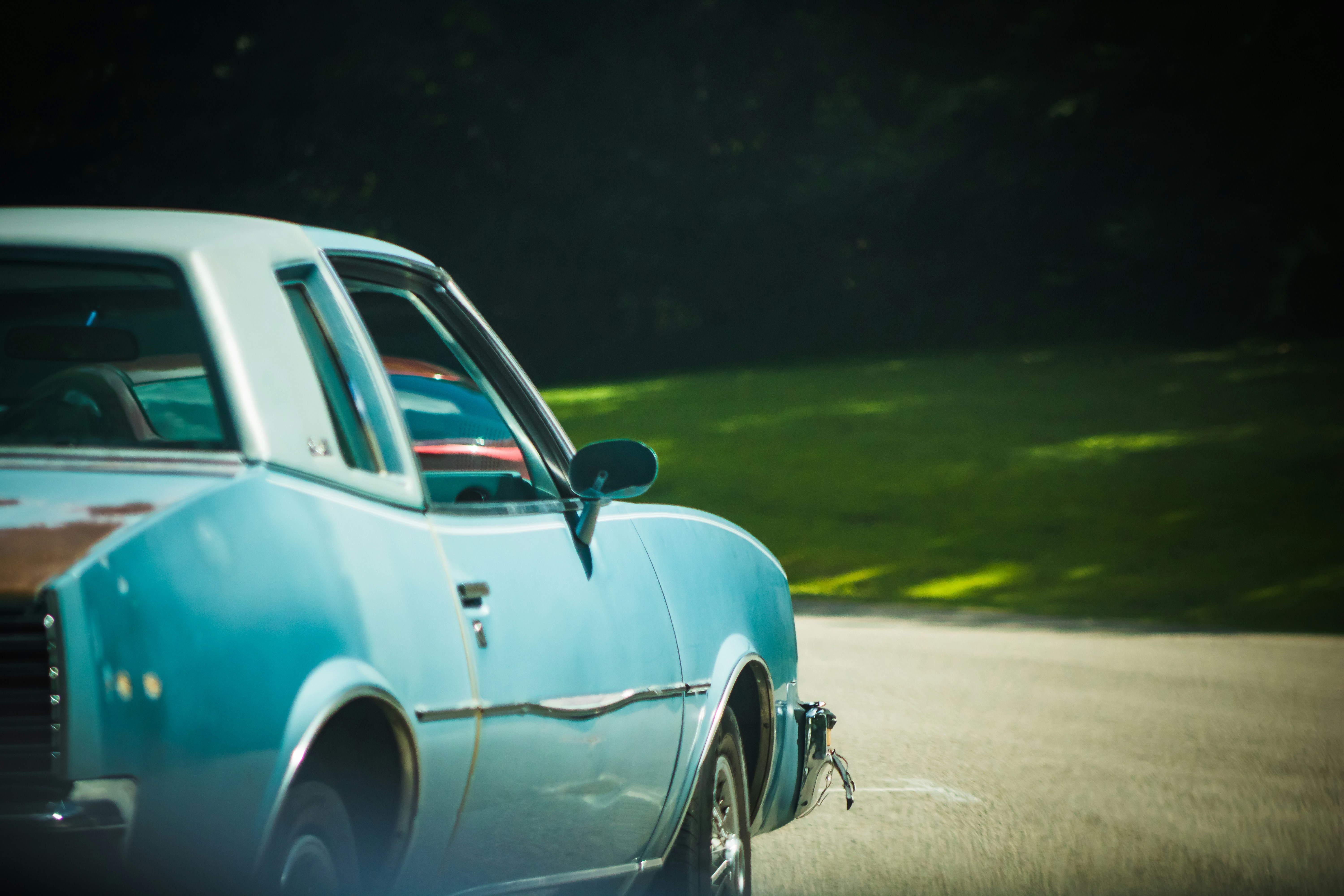 Blue Classic on a Sunlit Lane: a mid-angle glimpse of a vintage coupe against a verdant backdrop
