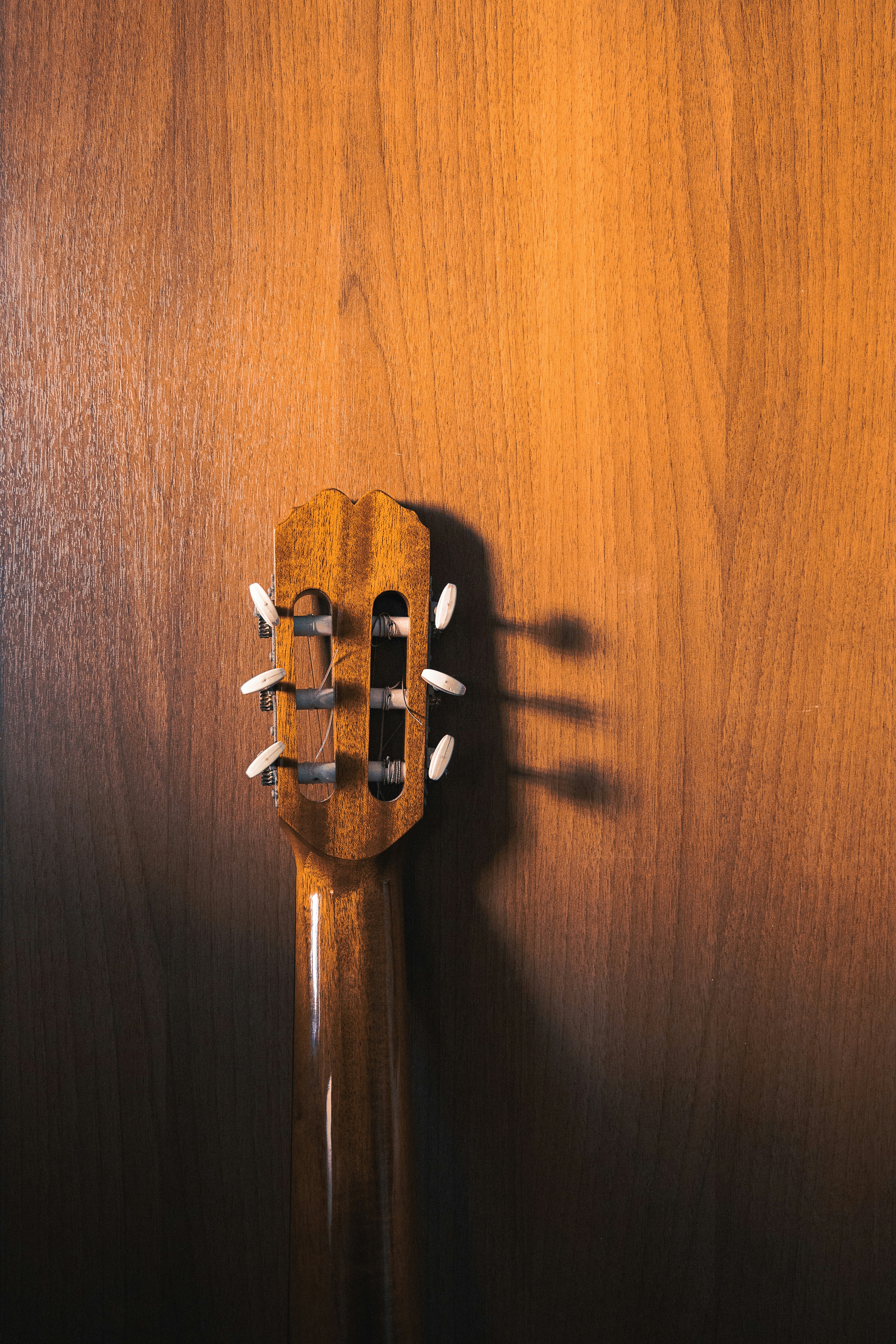 Close-up of a guitar headstock against a warm wooden background, highlighting its intricate tuning pegs and the play of light and shadow.