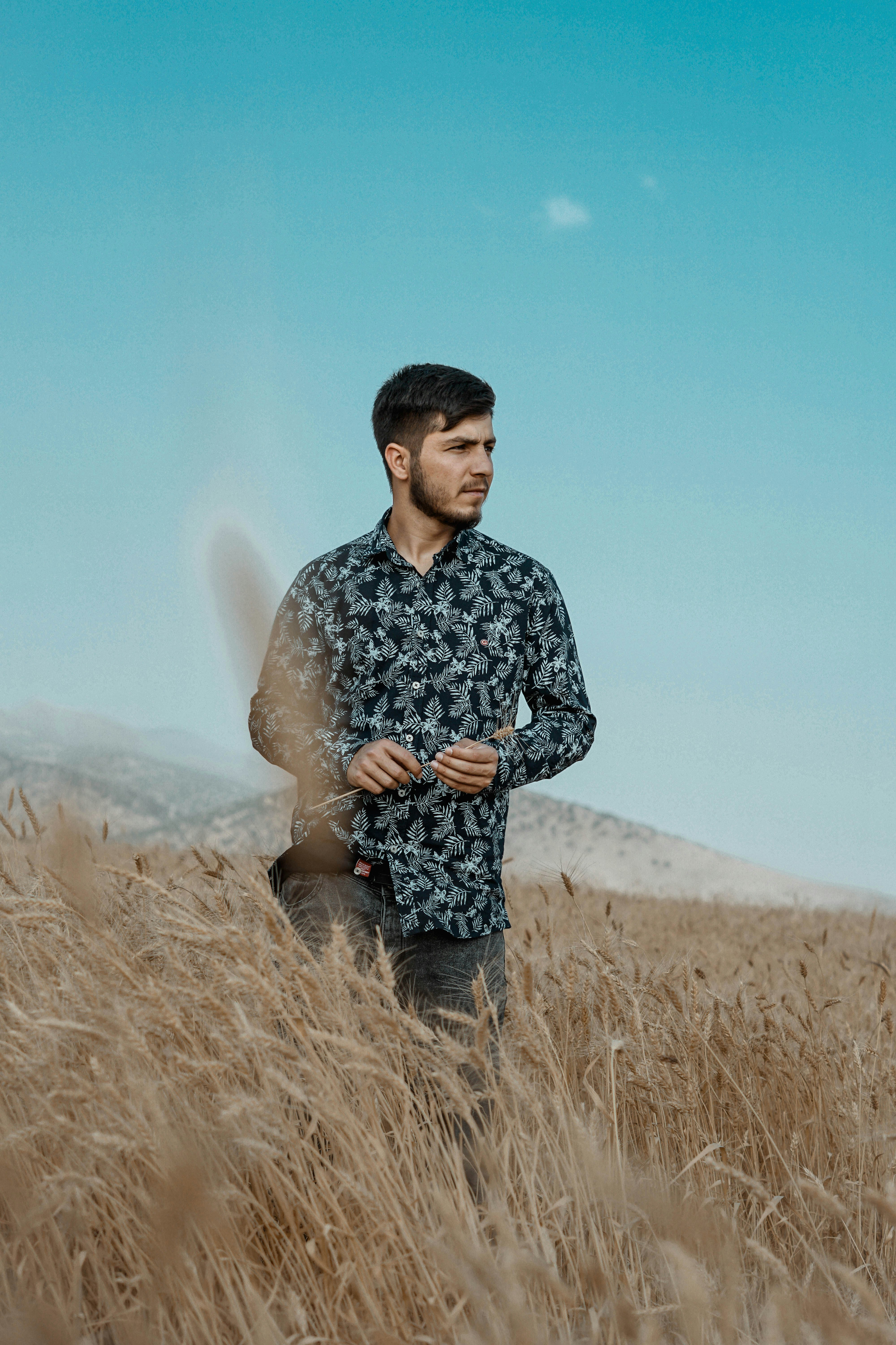 Man in black and white floral dress shirt standing on brown grass field ...