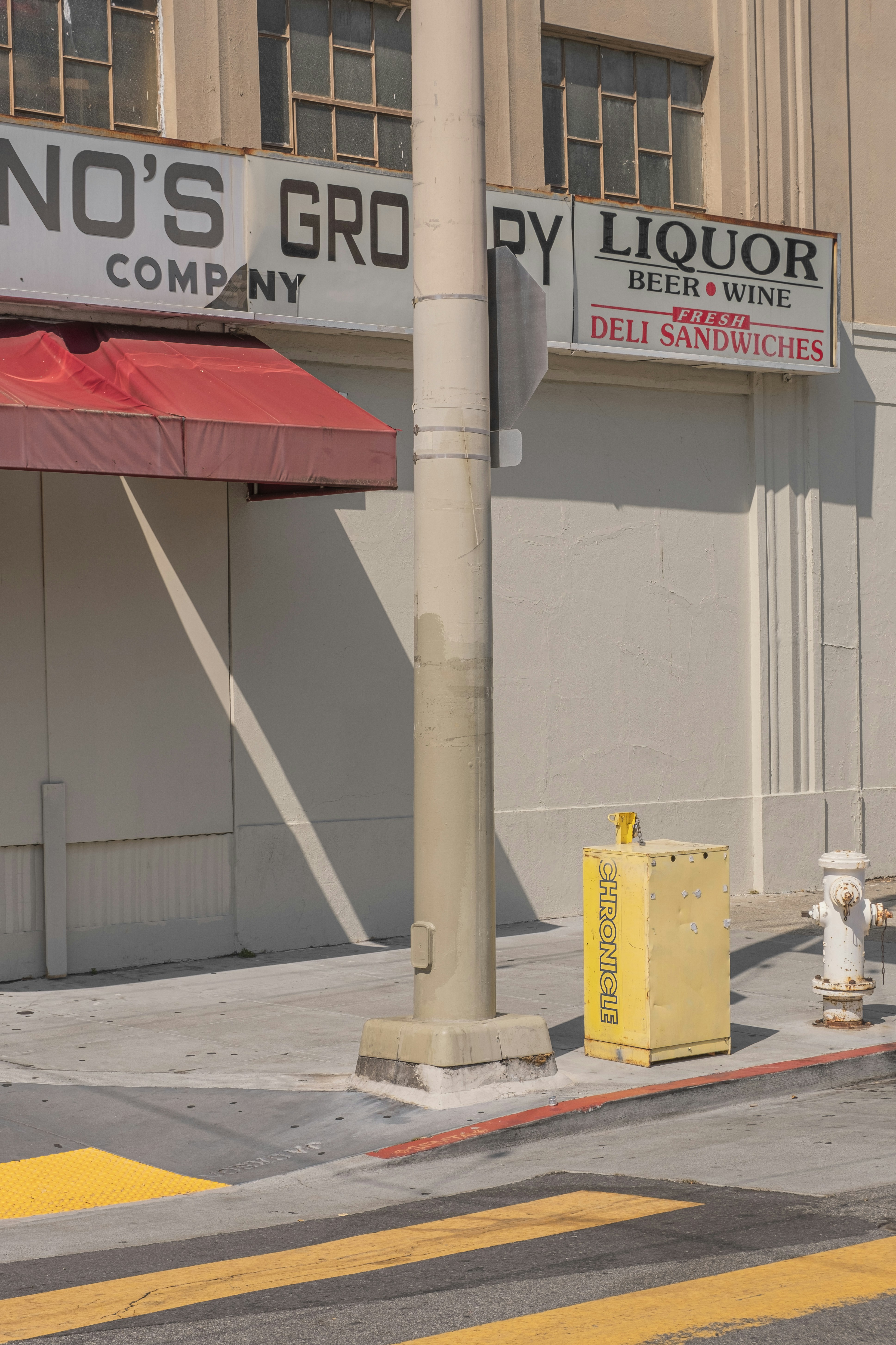 Exterior of a grocery store featuring signage for liquor, beer, and deli sandwiches, with a fire hydrant and yellow utility box nearby.