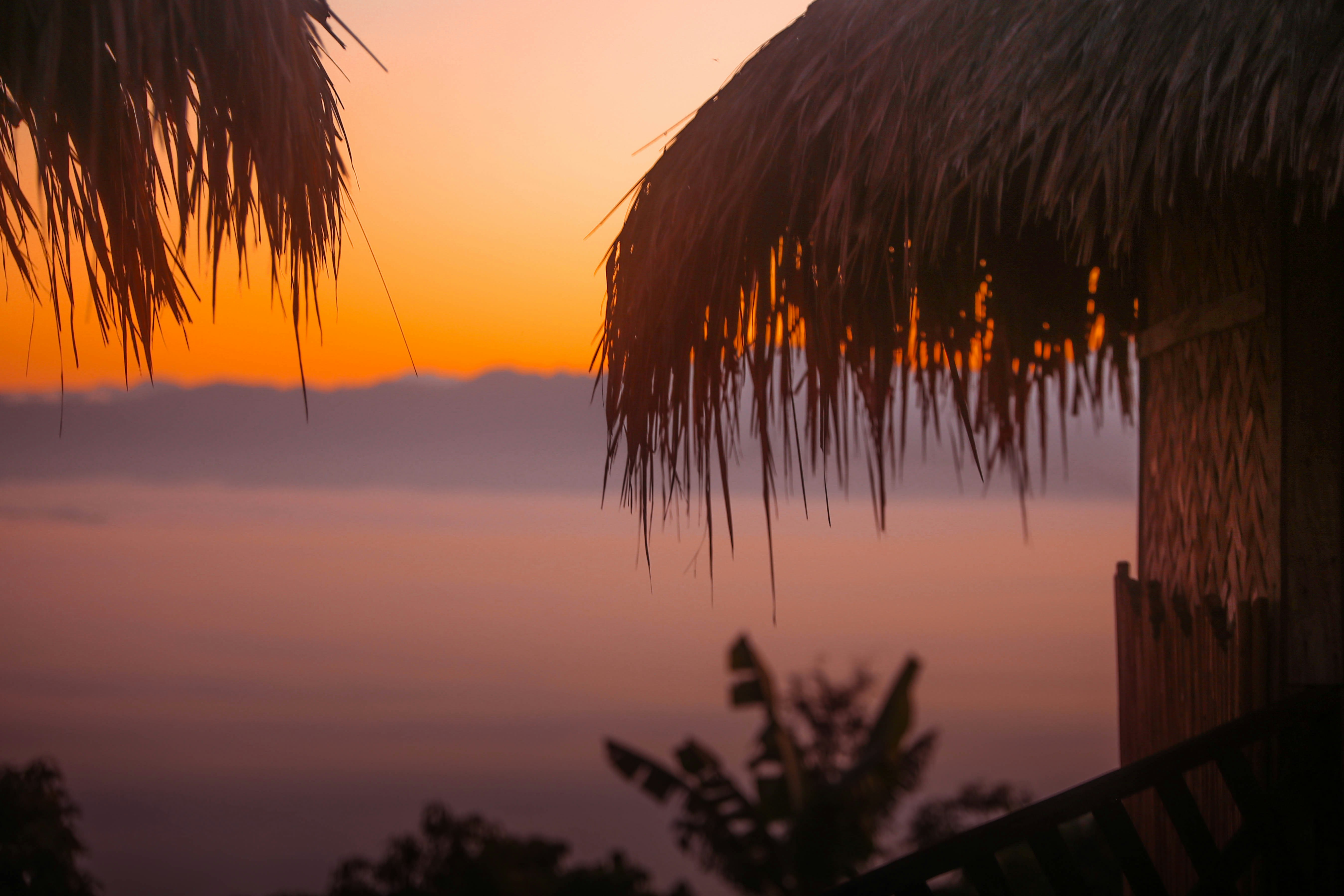 Sunset Over a Thatched Shelter: Silhouettes and Warm Horizons